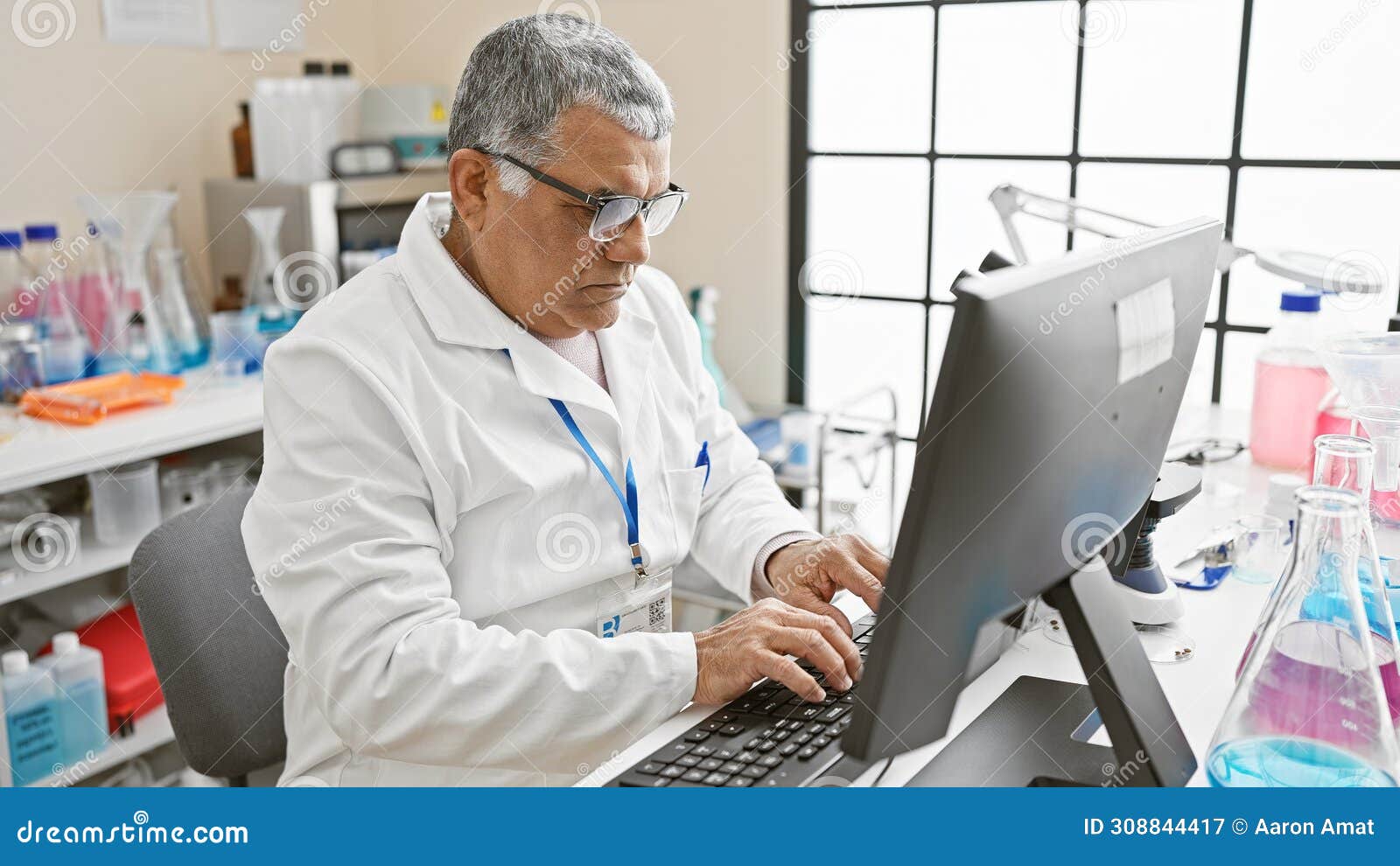 Mature Man in Lab Coat Analyzing Data on Computer in a Bright ...