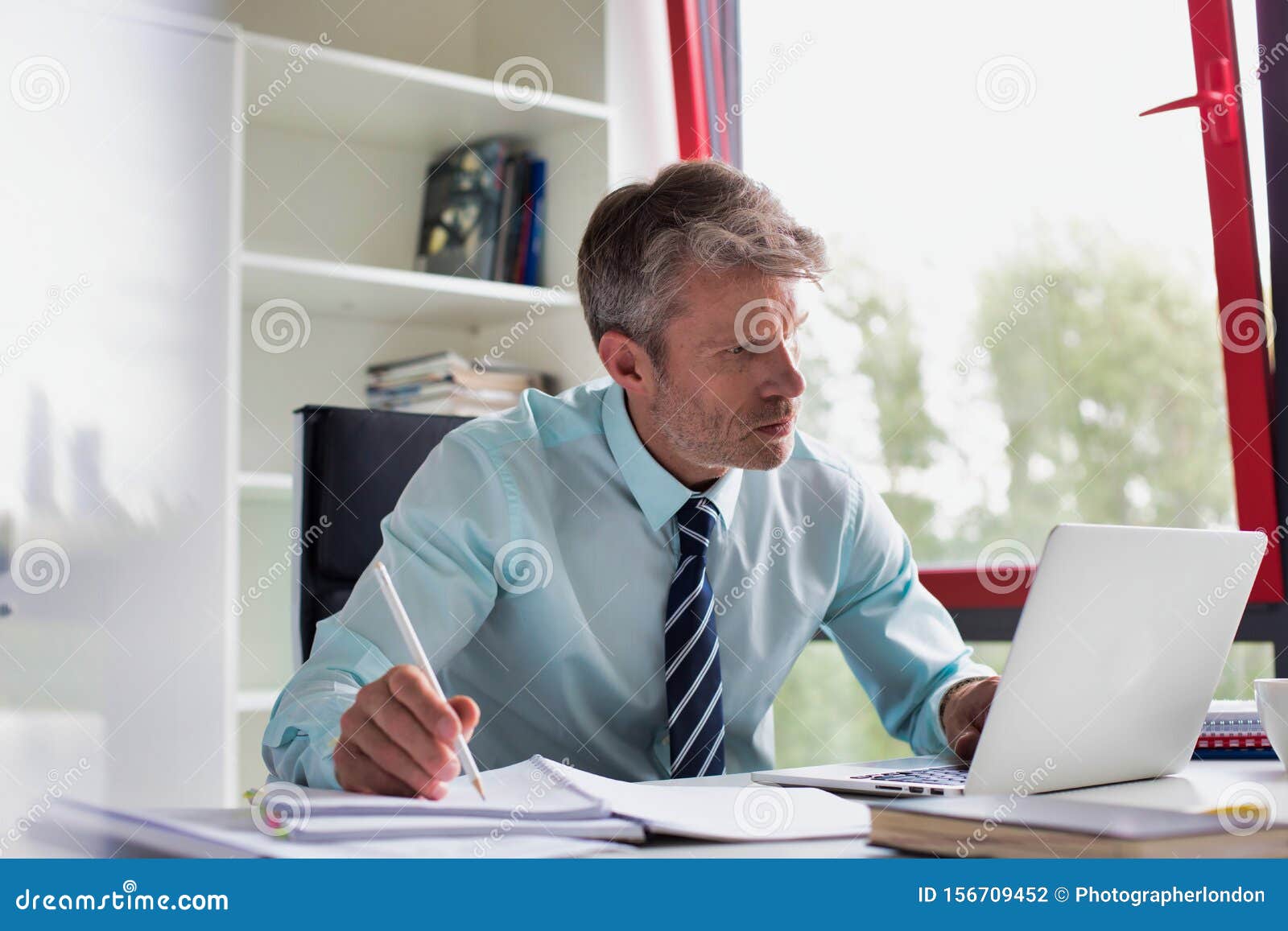 Mature Man Looking on Laptop while Writing on Notes in Office Stock ...