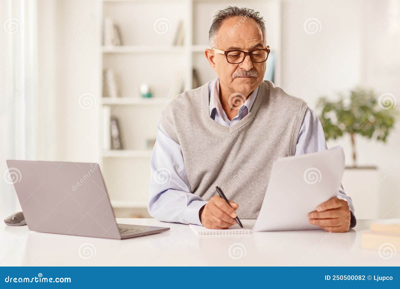 Mature Man Sitting in Front of a Laptop Computer Looking at a Paper ...