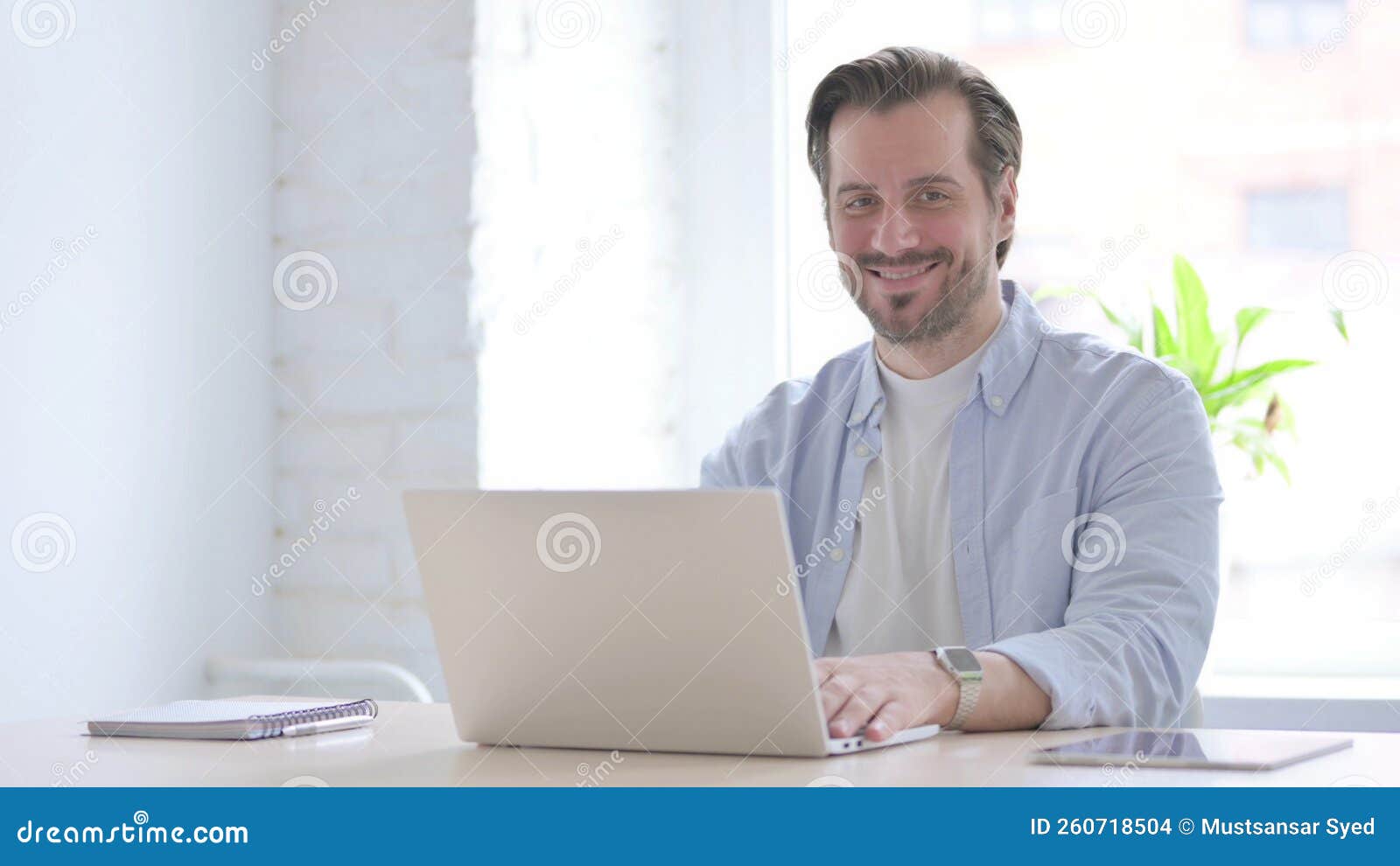 Young Man Smiling at Camera while Using Laptop Stock Photo - Image of ...