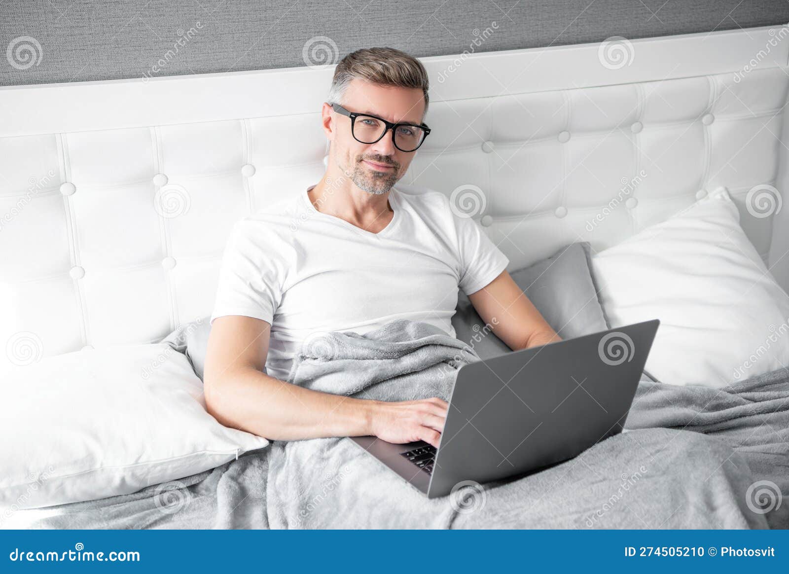 Mature Man Virtual Assistant in Glasses Working on Laptop in Bed Stock ...