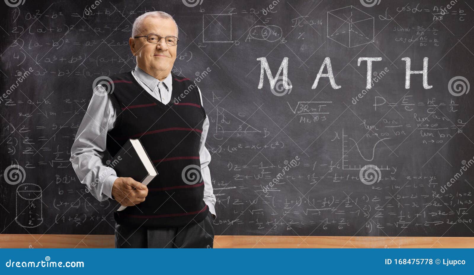 Mature Math Teacher with a Book in Front of a Blackboard with Formulas ...