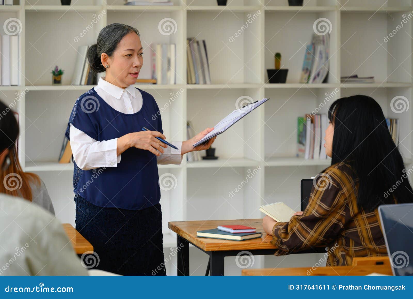 Mature Professor Explaining Something To Her Students in Library at ...
