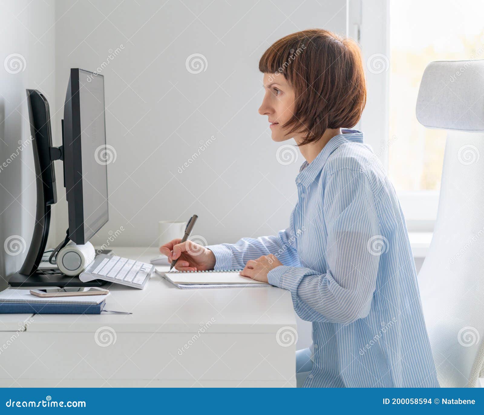 Mature Woman Looking at Computer Screen and Writing Information in ...