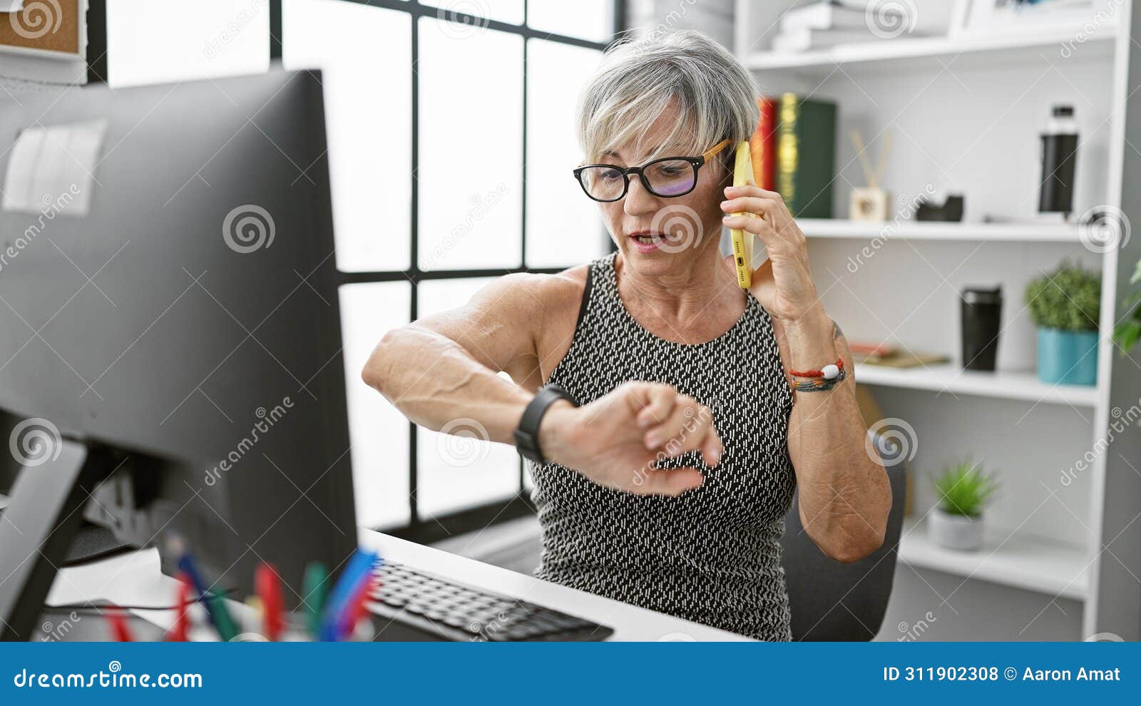 Mature Woman Multitasking in a Modern Office, Checking Time while on a ...
