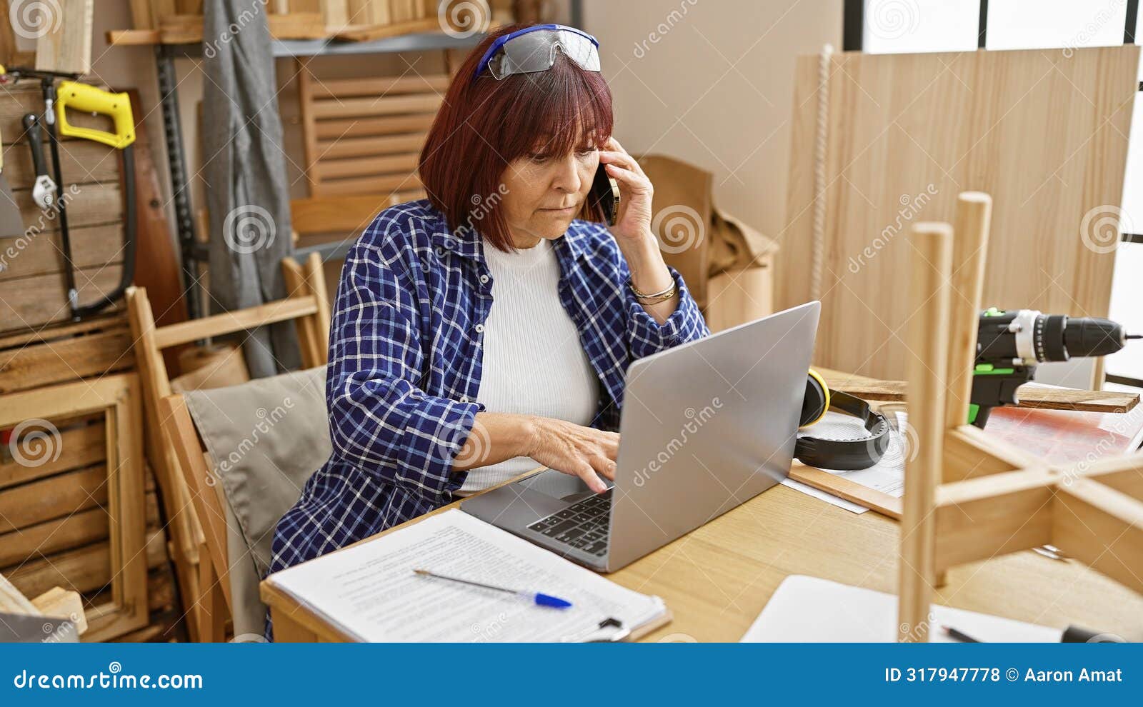 Mature Woman Multitasking on Phone and Laptop in a Carpentry Workshop ...