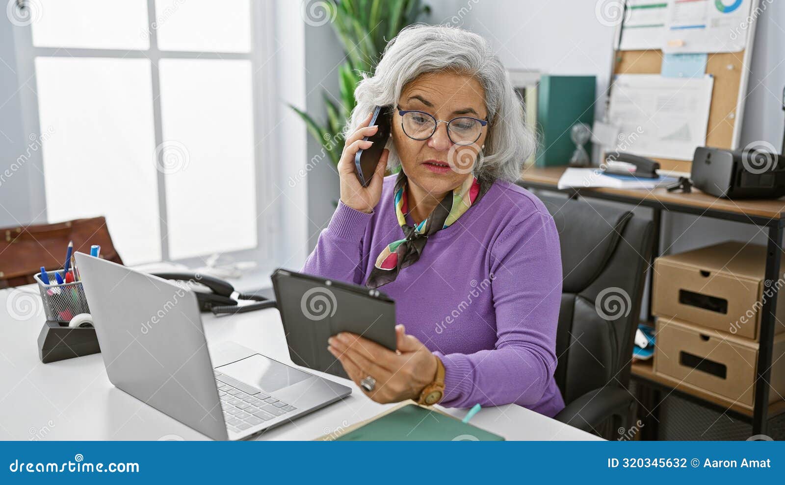 Mature Woman Multitasking with Phone and Tablet in a Modern Office ...