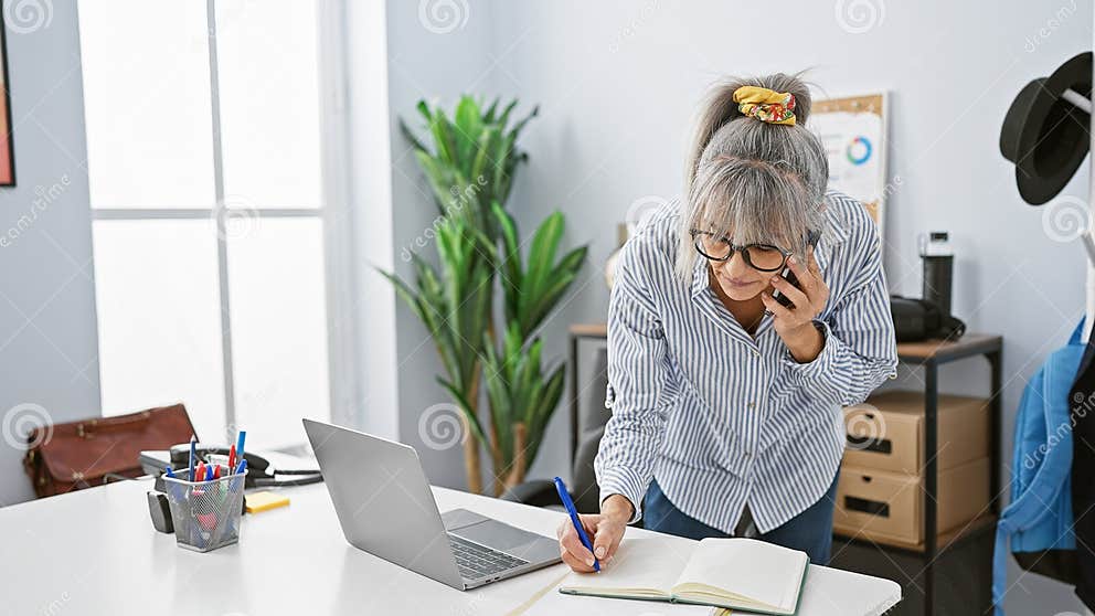 A Mature Woman Multitasks in a Modern Office, Talking on the Phone ...