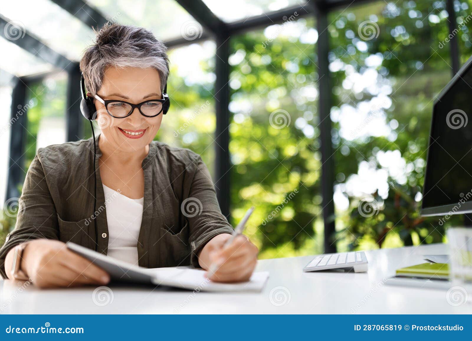 Mature Woman Sitting at Workplace in Front Computer, Using Headset ...