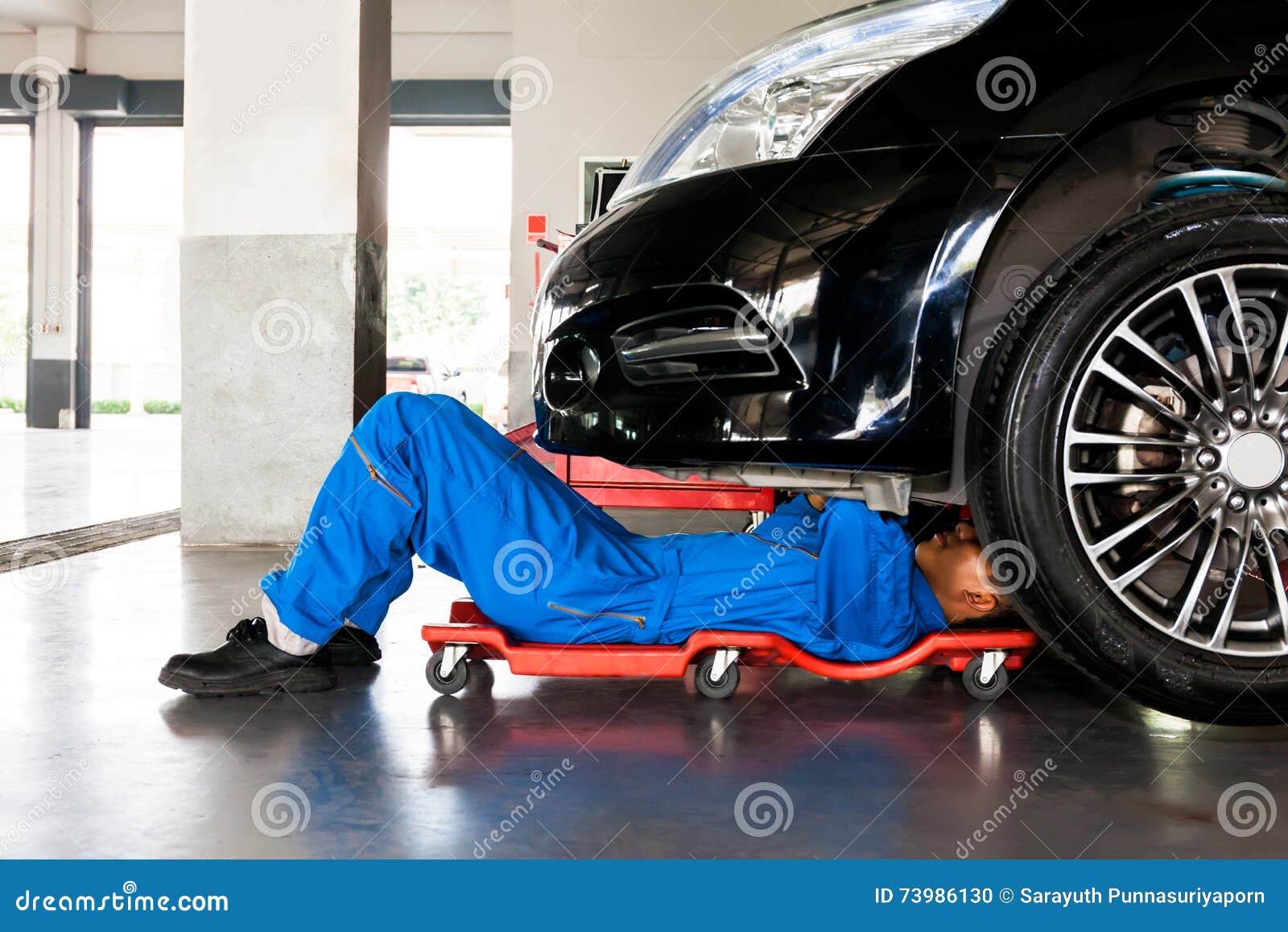 Mechanic in Blue Uniform Lying Down and Working Under Car at Auto ... Mechanic in Blue Uniform Lying Down and Working Under Car at Auto ...