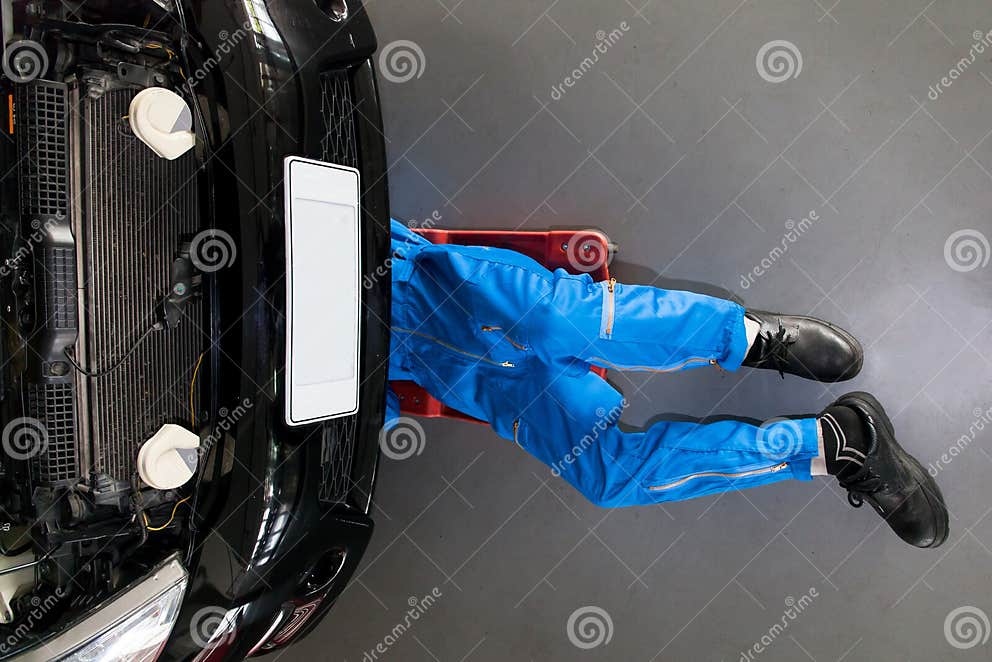 Mechanic in Blue Uniform Lying Down and Working Under Car at the Stock ...