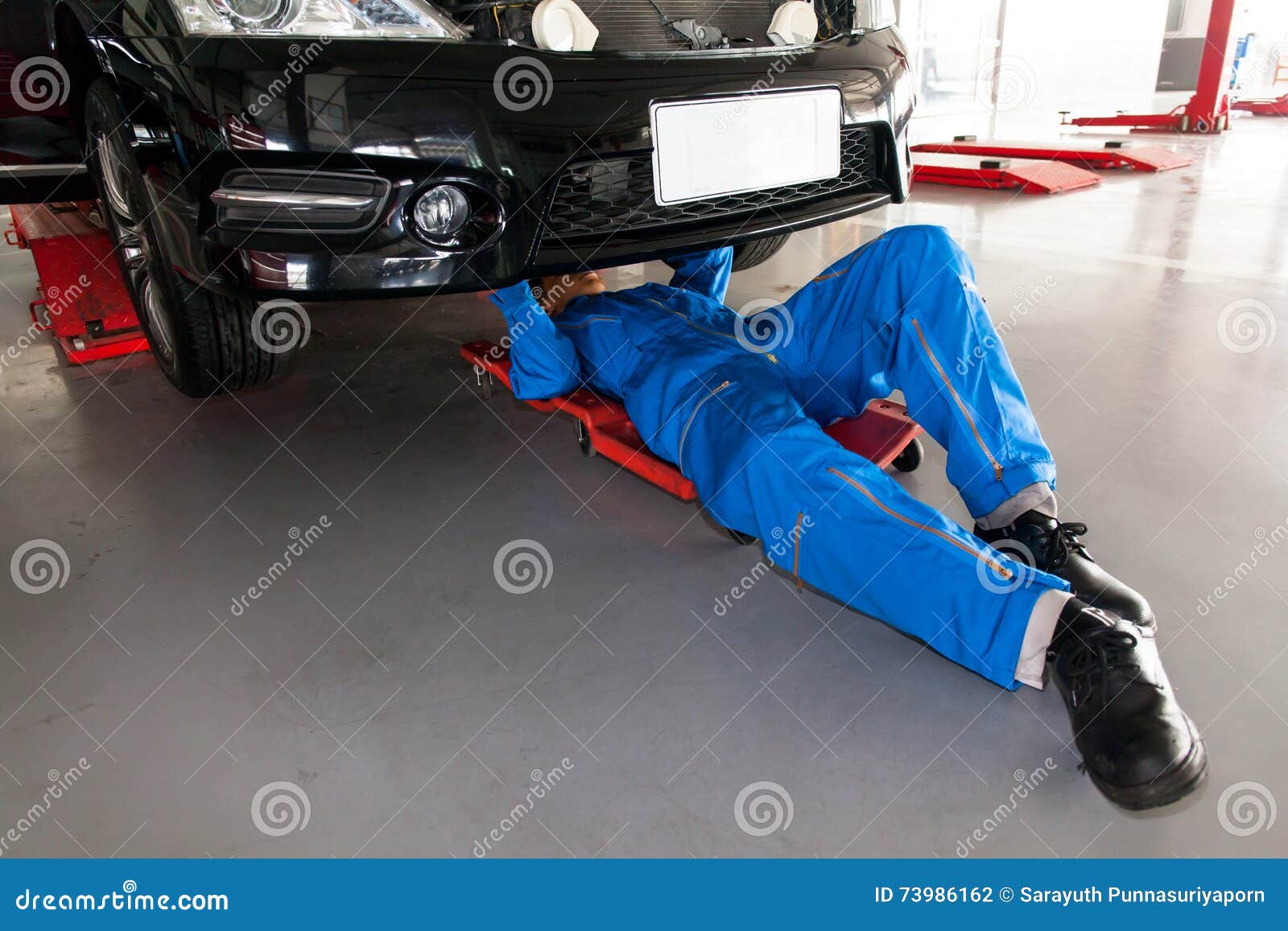Mechanic in Blue Uniform Lying Down and Working Under Car at the Stock ...