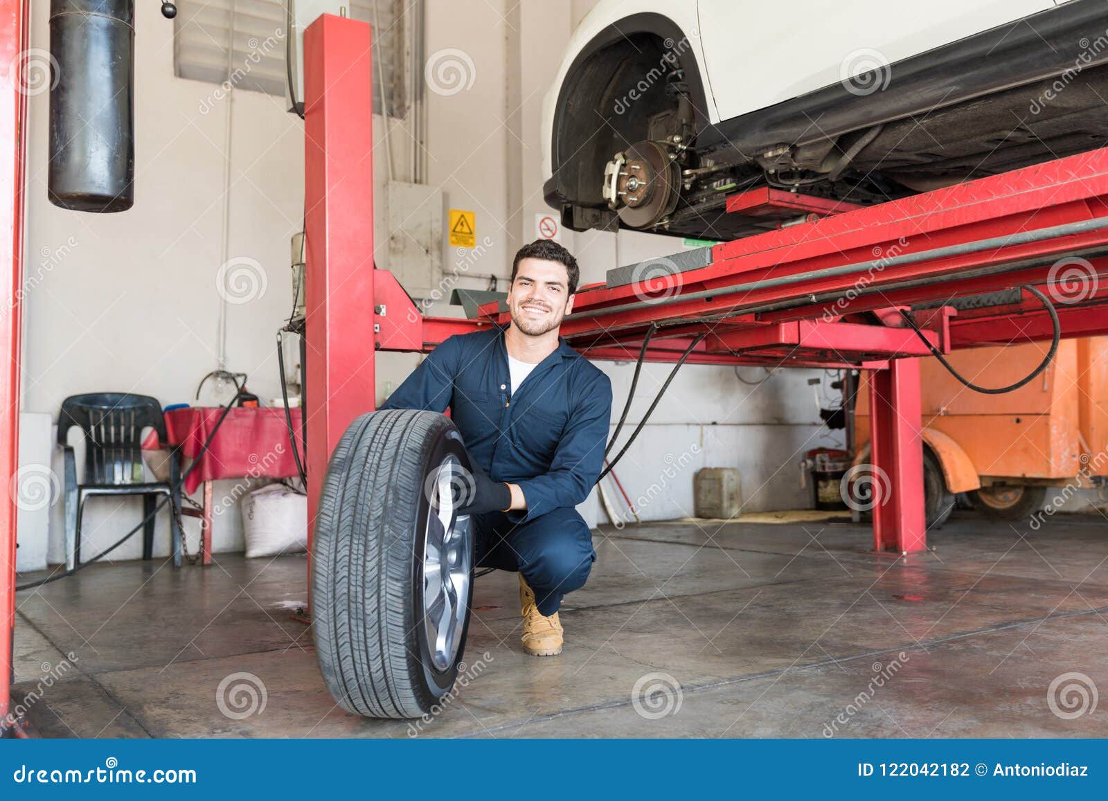 Mechanic Examining Car Tire while Crouching in Workshop Stock Photo ...