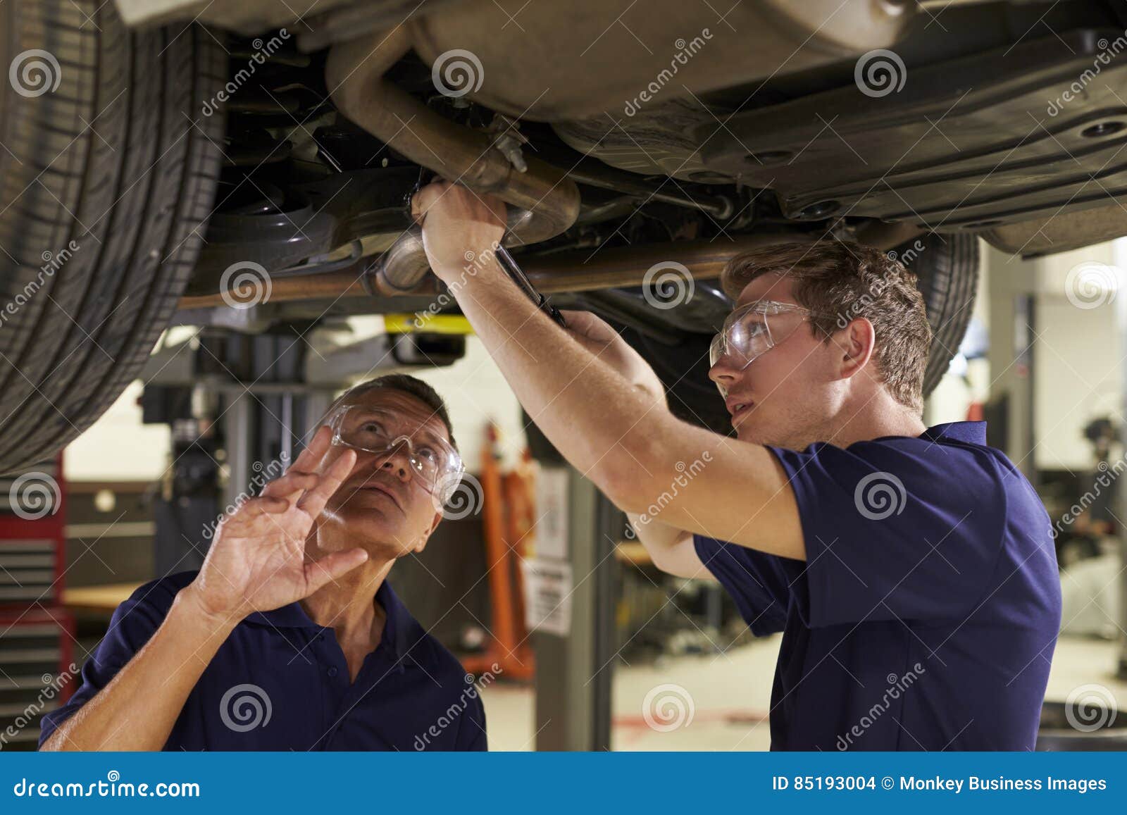 Mechanic and Male Trainee Working Underneath Car Together Stock Photo ...
