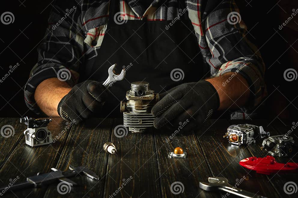 A Mechanic at a Workbench in a Workshop Repairs an Old Chainsaw Engine ...