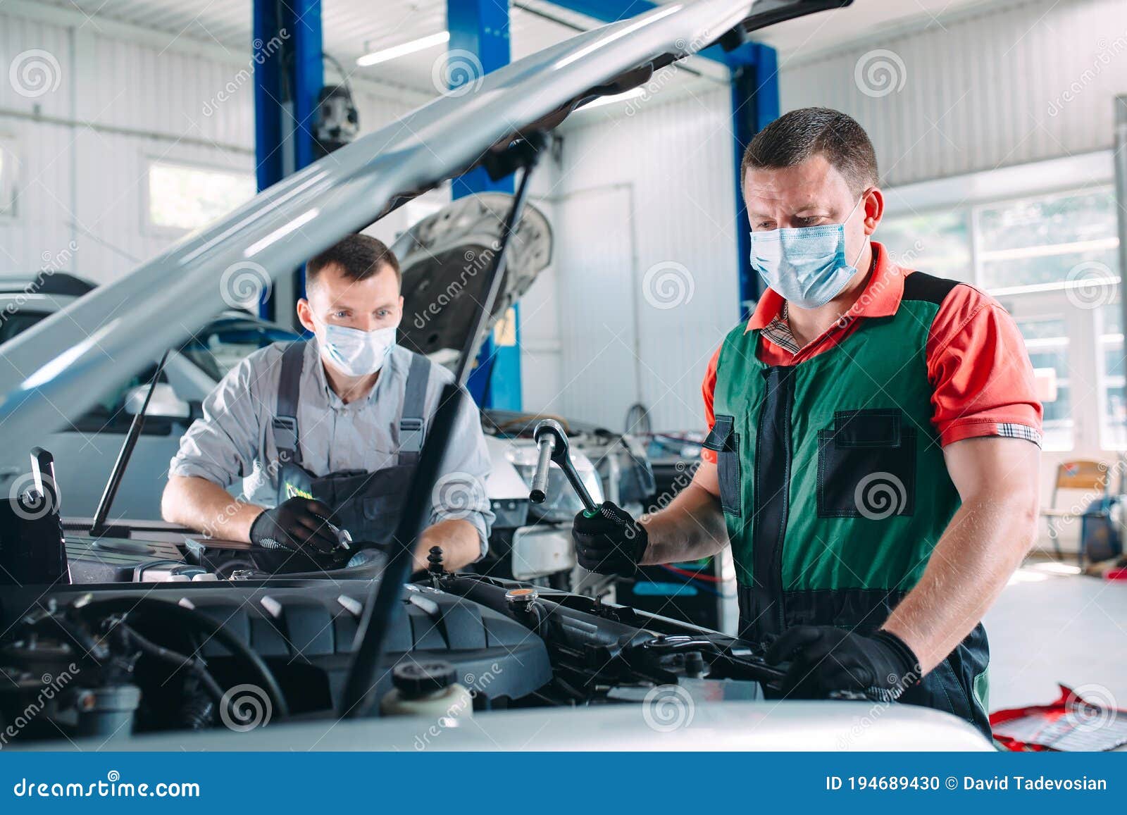 Mechanics in Uniform and Protective Masks Work in a Car Workshop. Stock ...
