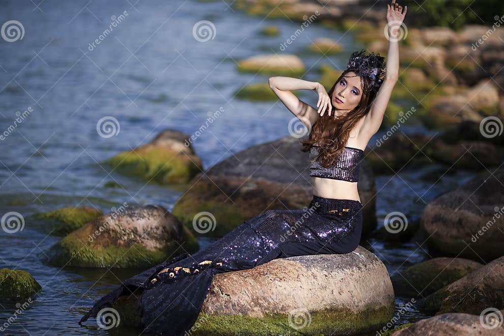 Mermaid Posing Near Ocean Shore On Rocks While Wearing Seashell