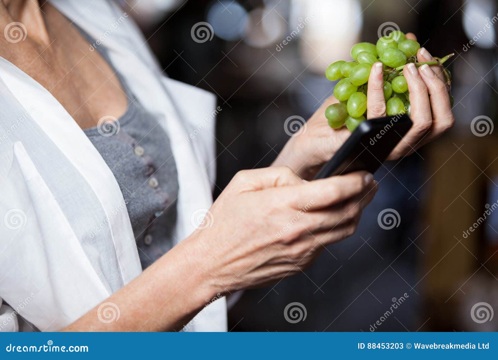 Mid Section of Female Costumer Holding Grapes while Using Mobile Phone ...