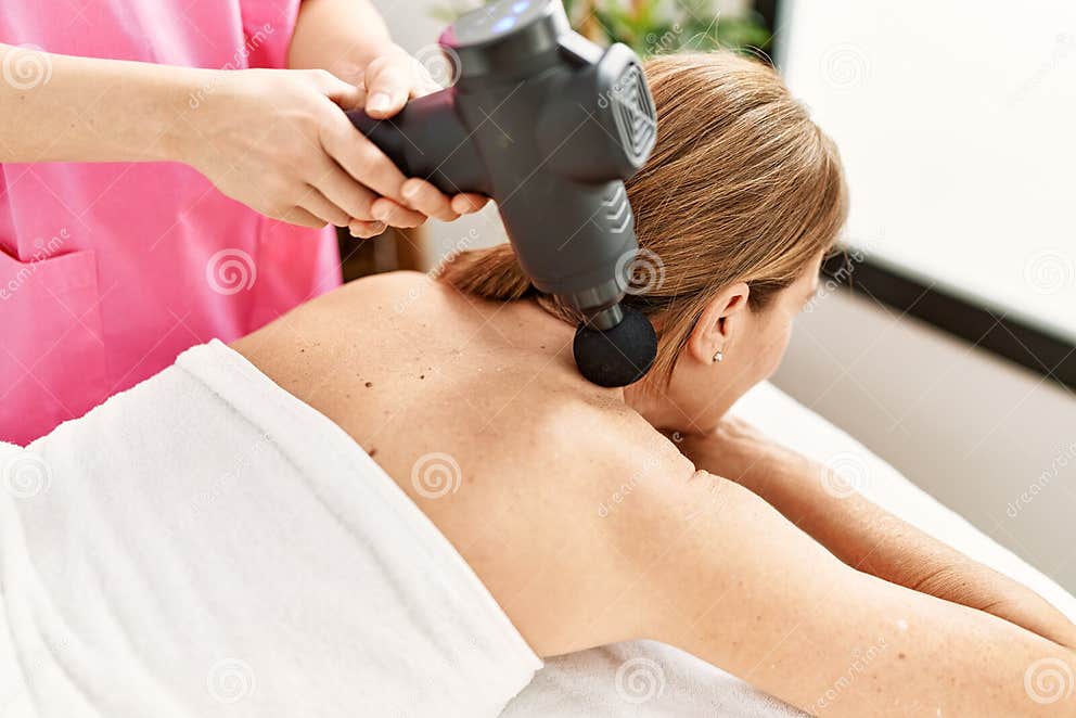 Middle Age Caucasian Woman Having Back Massage Using Percussion Pistol At Beauty Center Stock