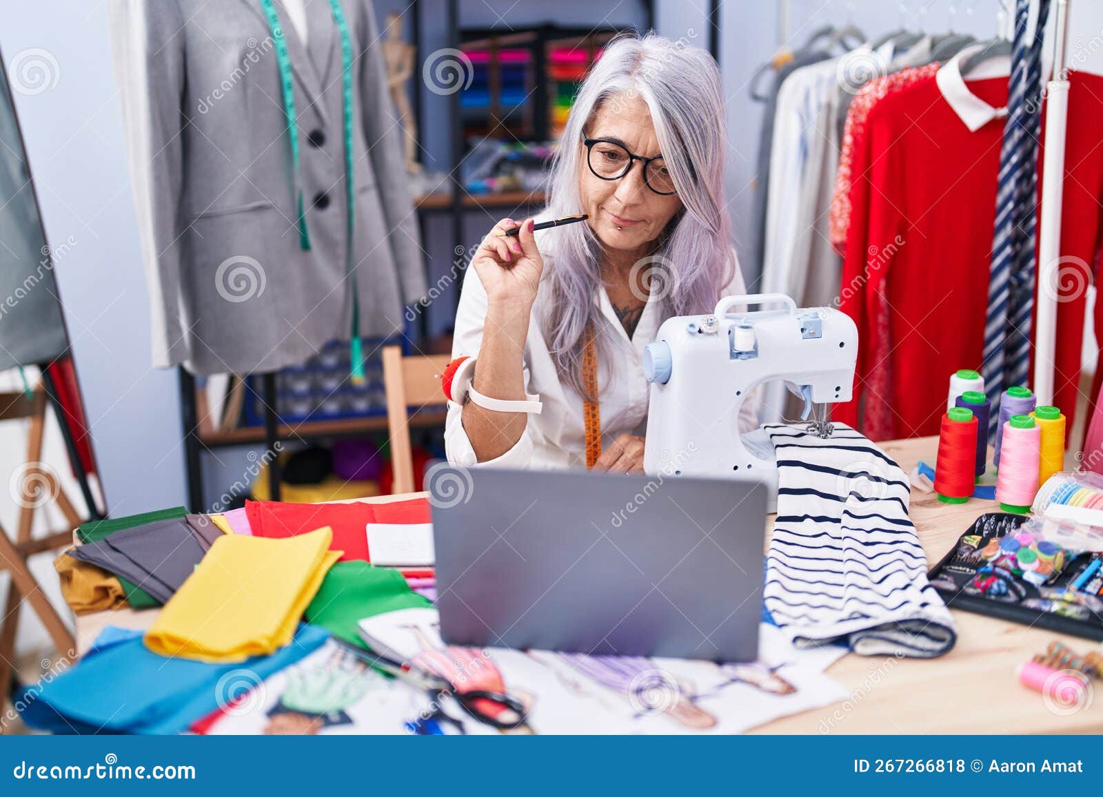 Middle Age Grey-haired Woman Tailor Using Sewing Machine and Laptop at ...