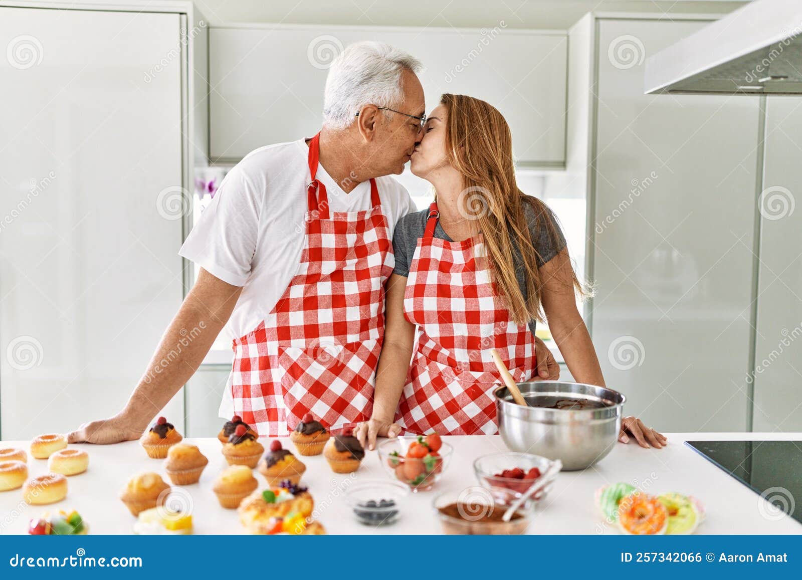 Middle Age Hispanic Couple Kissing and Cooking Sweets at the Kitchen ...