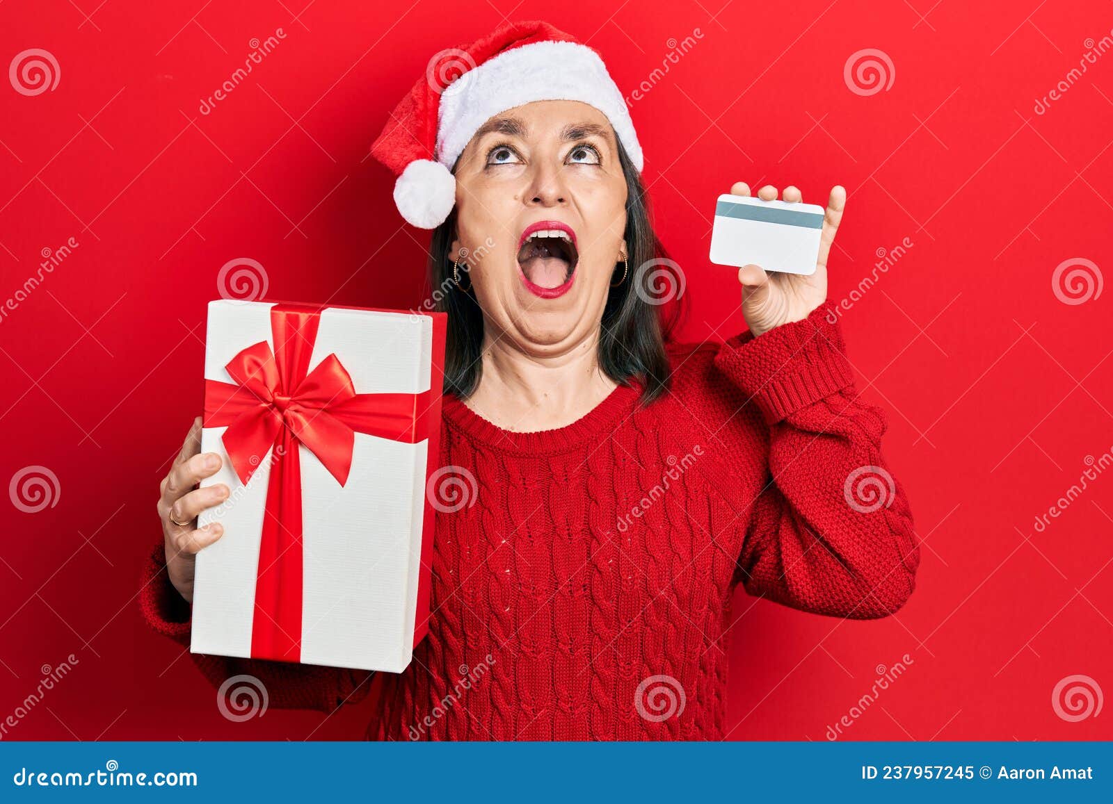 Middle Age Hispanic Woman Wearing Christmas Hat Holding T And Credit