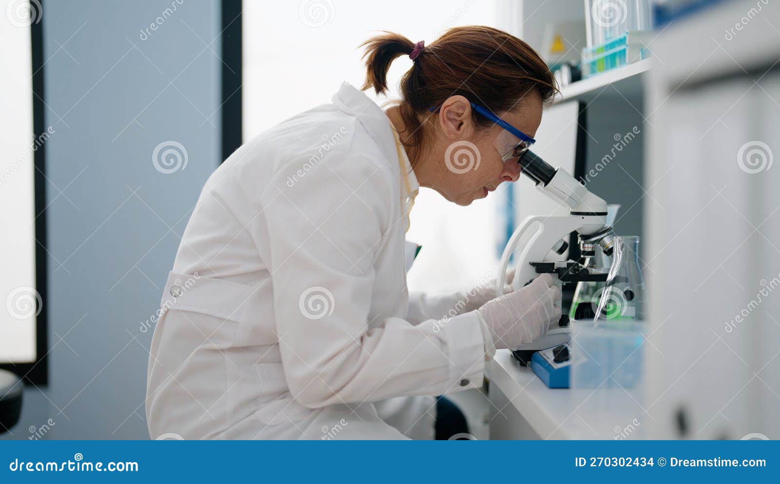 Middle Age Hispanic Woman Wearing Scientist Uniform Using Microscope at ...