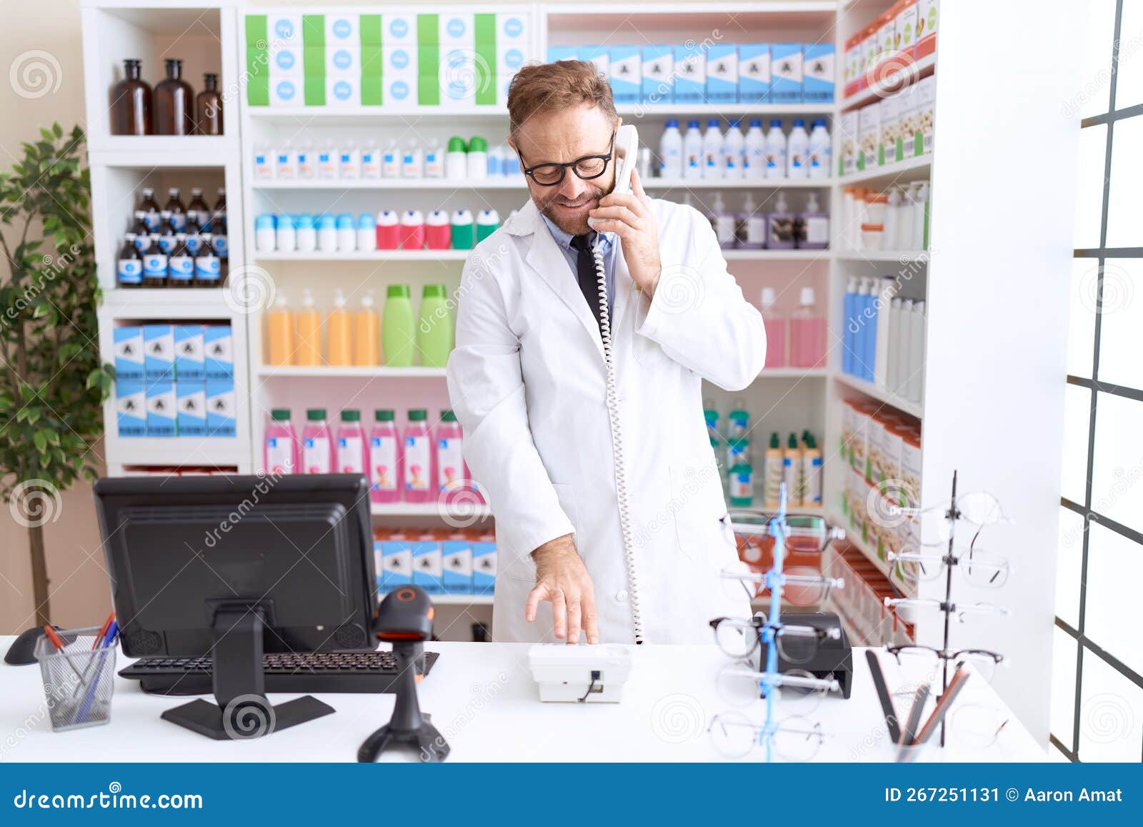 Middle Age Man Pharmacist Talking on Telephone Using Computer at ...