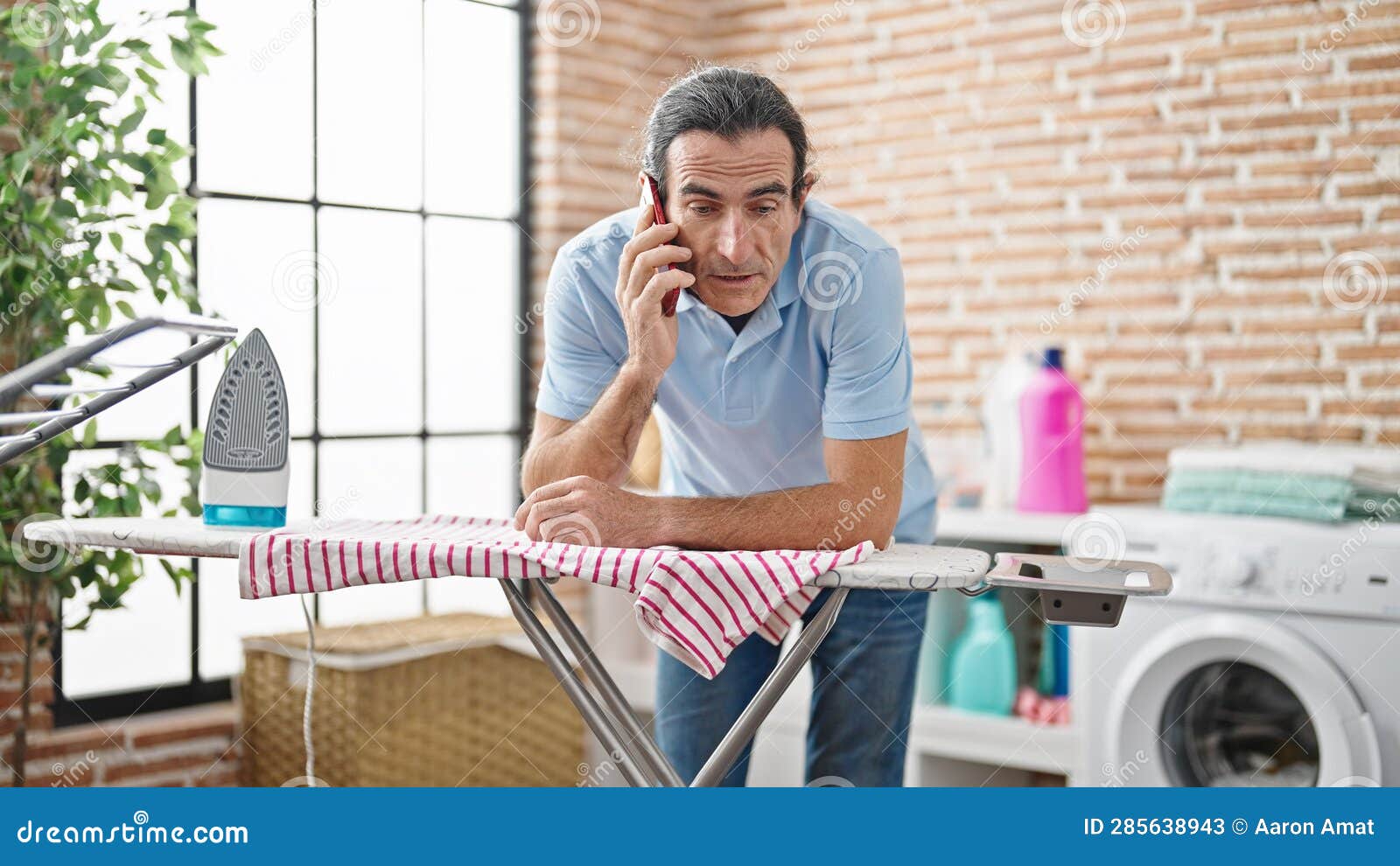 Middle Age Man Talking on Smartphone Leaning on Ironing Machine at ...