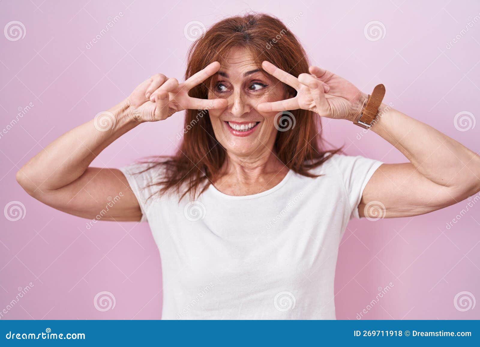 Middle Age Woman Standing Over Pink Background Doing Peace Symbol With Fingers Over Face