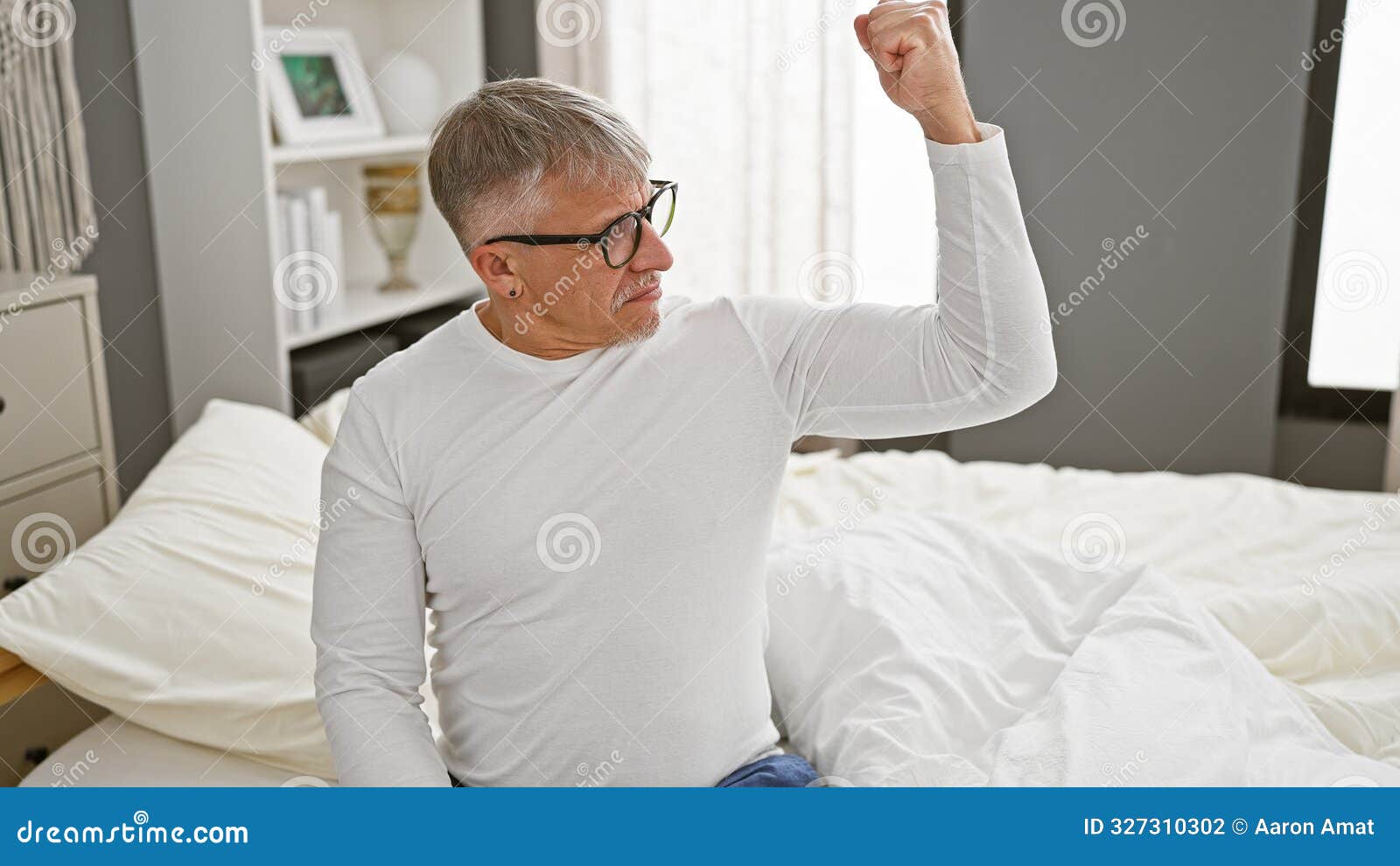 Middle-aged Man Flexing Muscles while Sitting on a White Bed in a ...