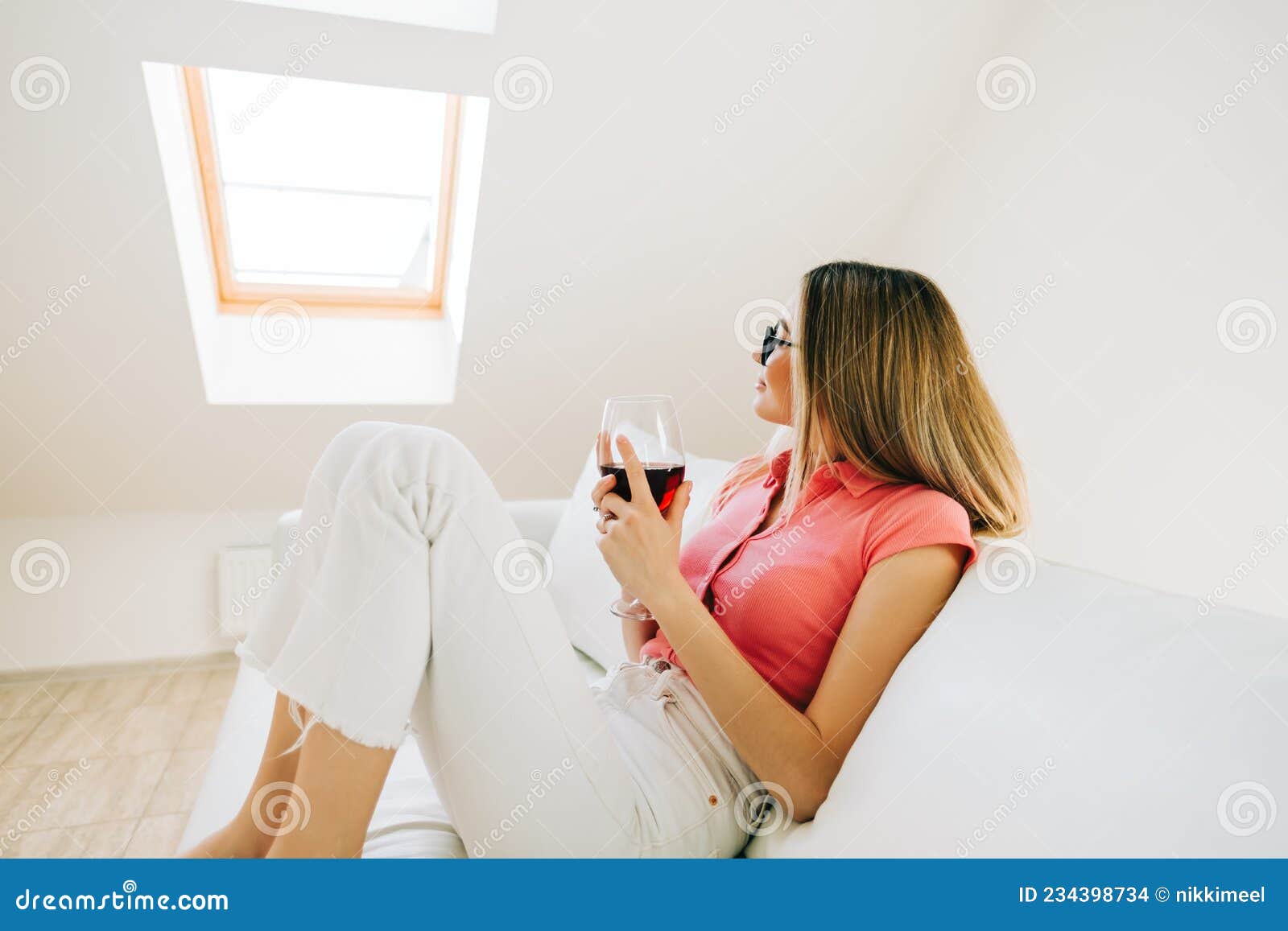 Millennial Woman Sitting On A Sofa In New Bright Apartment And Drinking