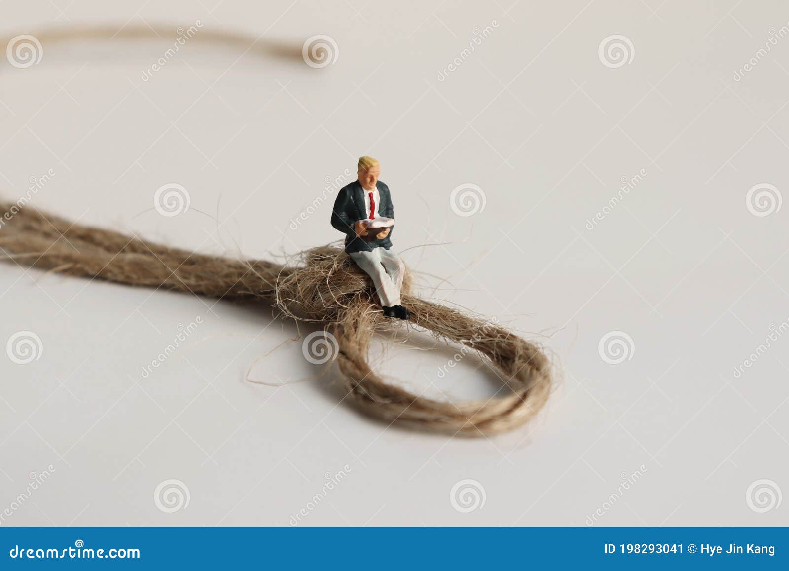 A Miniature Man Sitting on a Strapped Rope and Reading. Stock Image ...