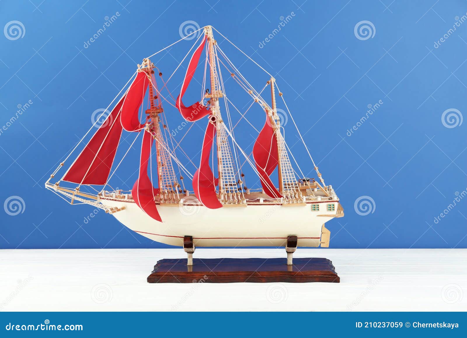 Miniature Model of Old Ship with Red Sails on White Table Against Blue ...