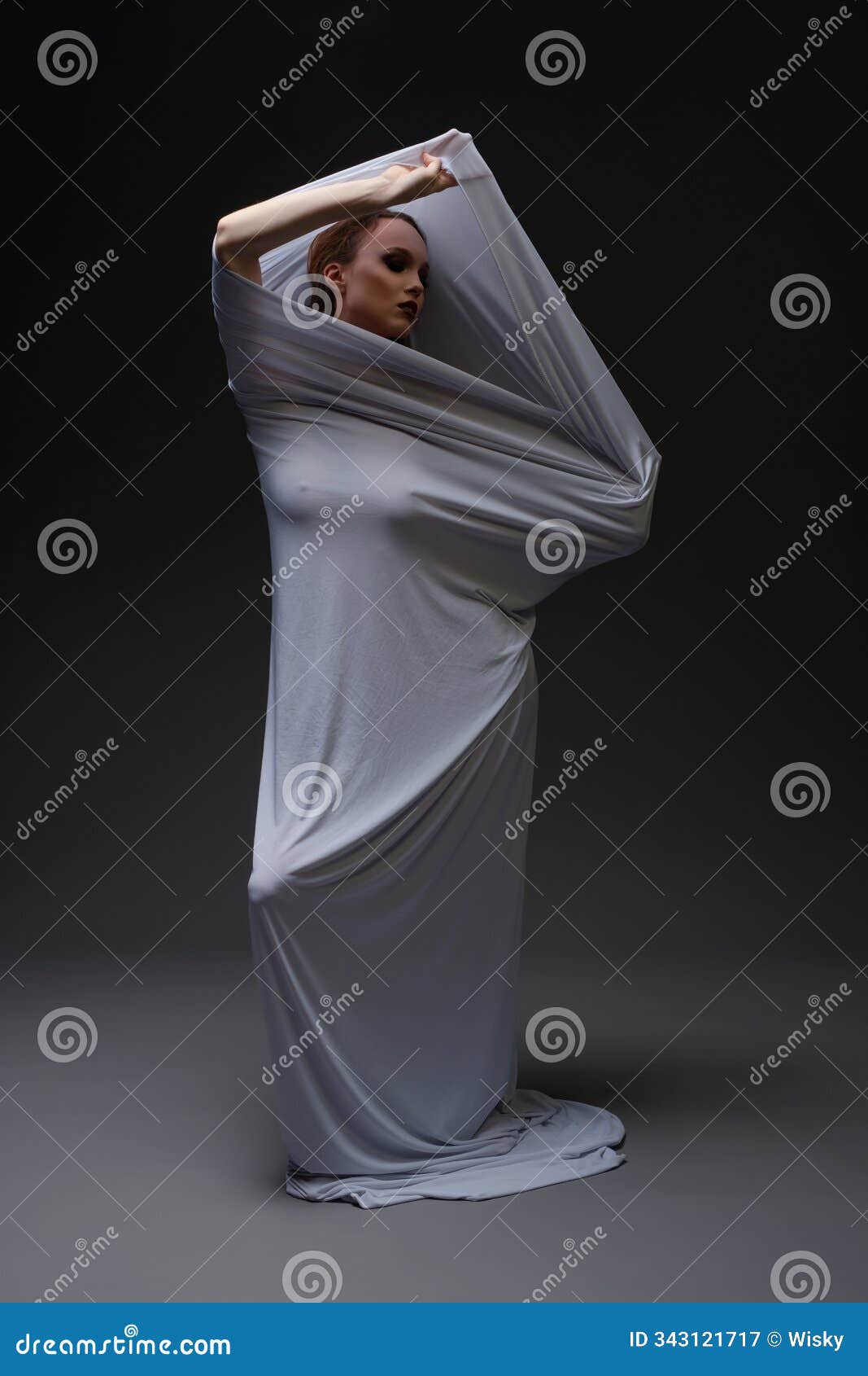 A Model Gracefully Poses in a Draped White Fabric in a Dark Studio ...