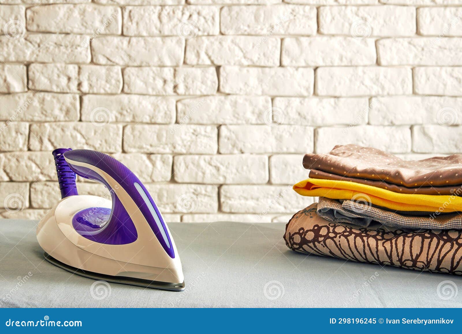 Modern Electric Iron on an Ironing Board with a Stack of Ironed Clothes ...