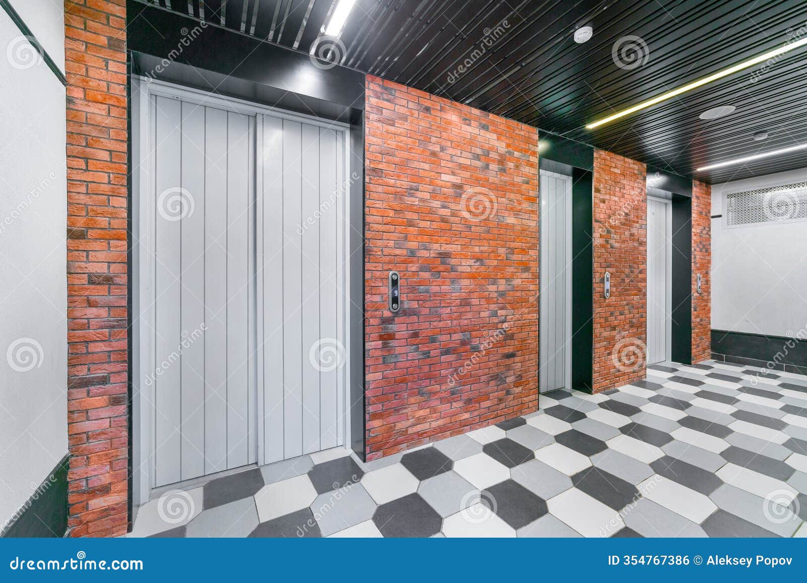 A Modern Elevator Lobby with Three Elevator Doors Set in a Brick Wal ...