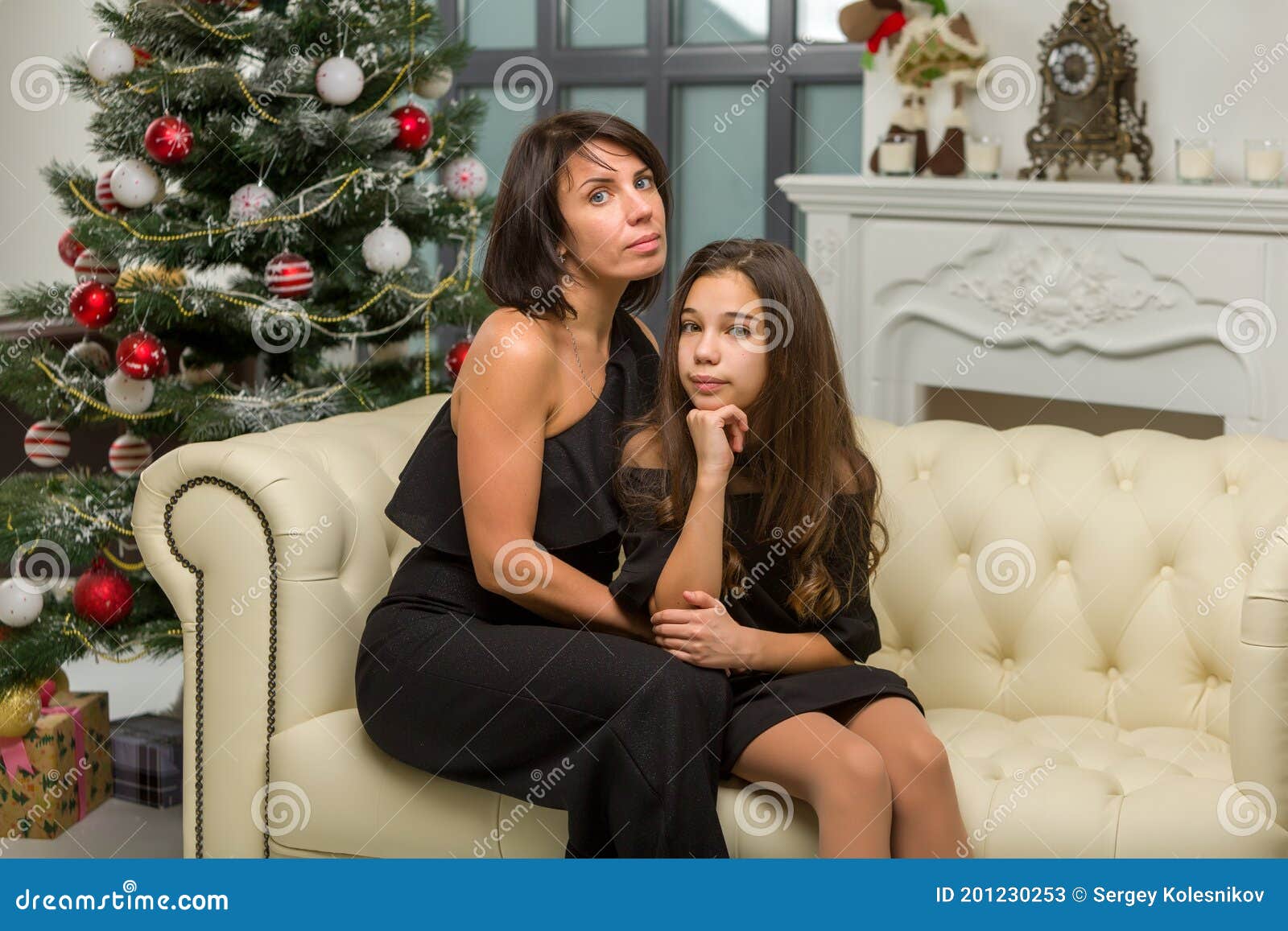 Mom And Daughter Near The Christmas Tree Are Sitting On The Couch