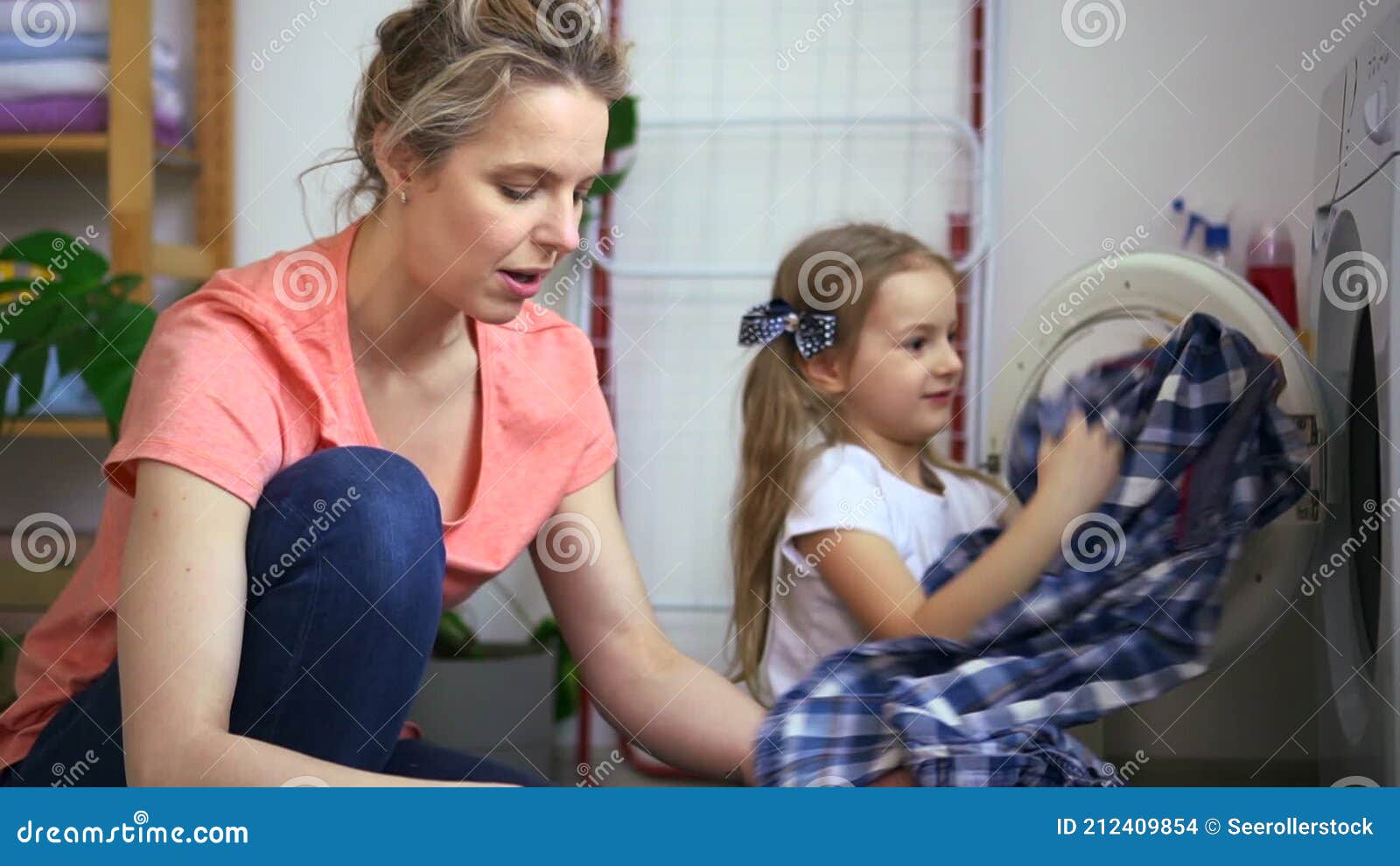 Mom And Daughter Putting Clothes In Washing Machine While Sitting In