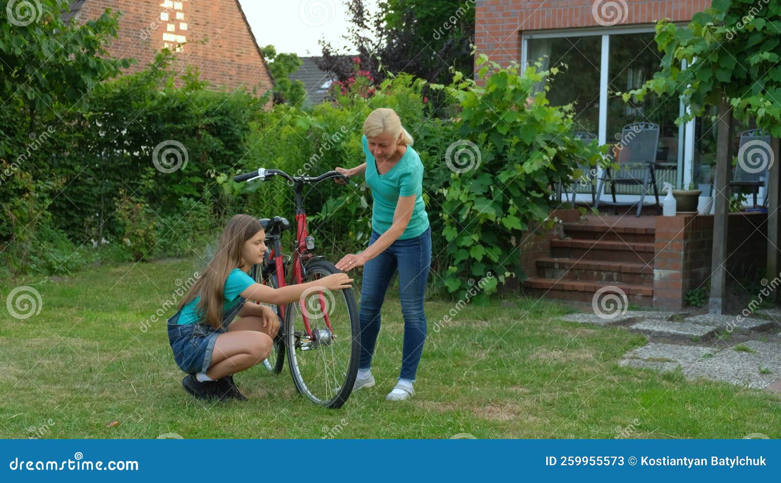 Mom Helps Her Daughter Fix Her Bicycle In The Backyard Of The House