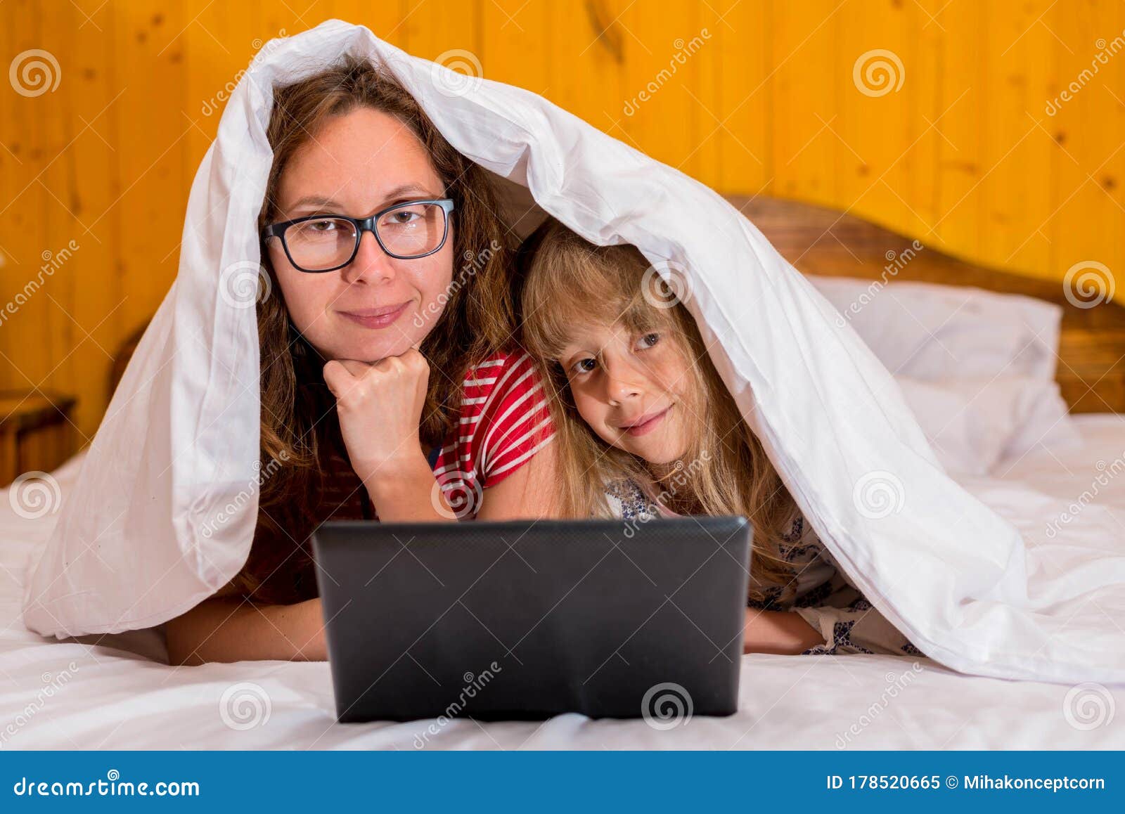 Mom And Little Daughter Lying In Bed Under A Blanket And Looking At A Laptop Stock Image Image