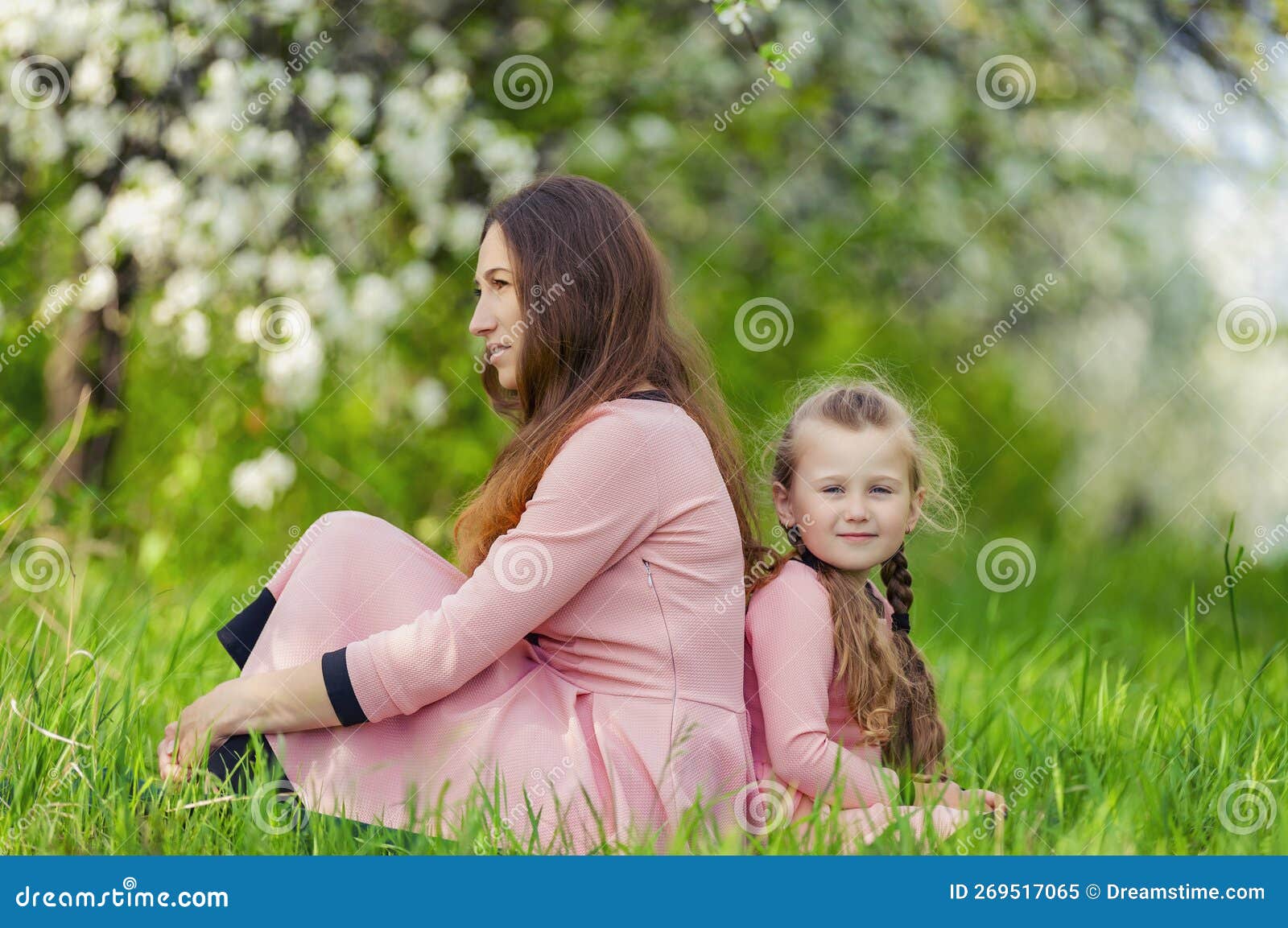 Mother And Daughter Sitting In Nature With Their Backs To Each Other