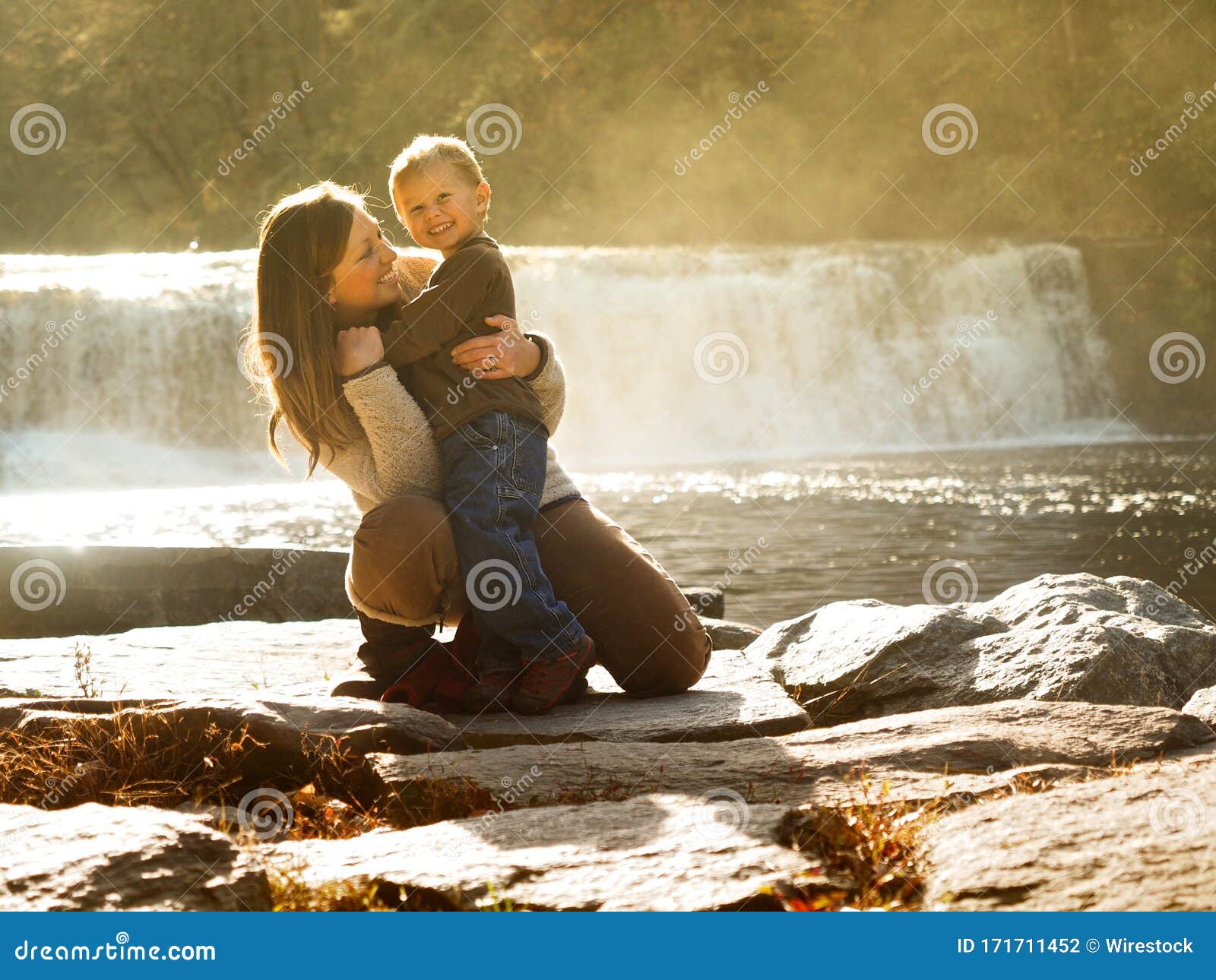 Mother Hugging Her Son in a Park Surrounded by Greenery and a Waterfall ...