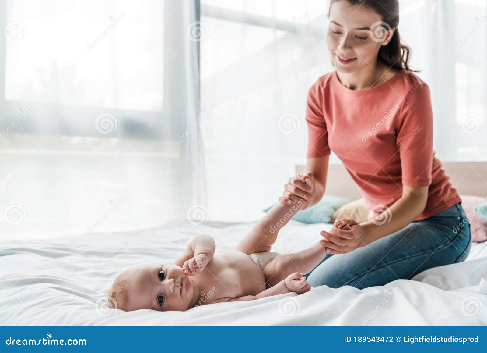 Mother Touching Legs of Baby Lying on Bed Stock Photo - Image of ...