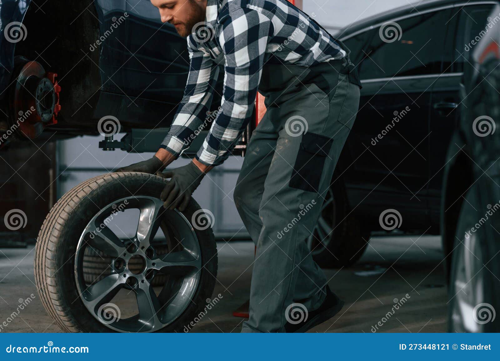 Moving the New Tire for a Car. Man in Uniform is Working in the Auto ...
