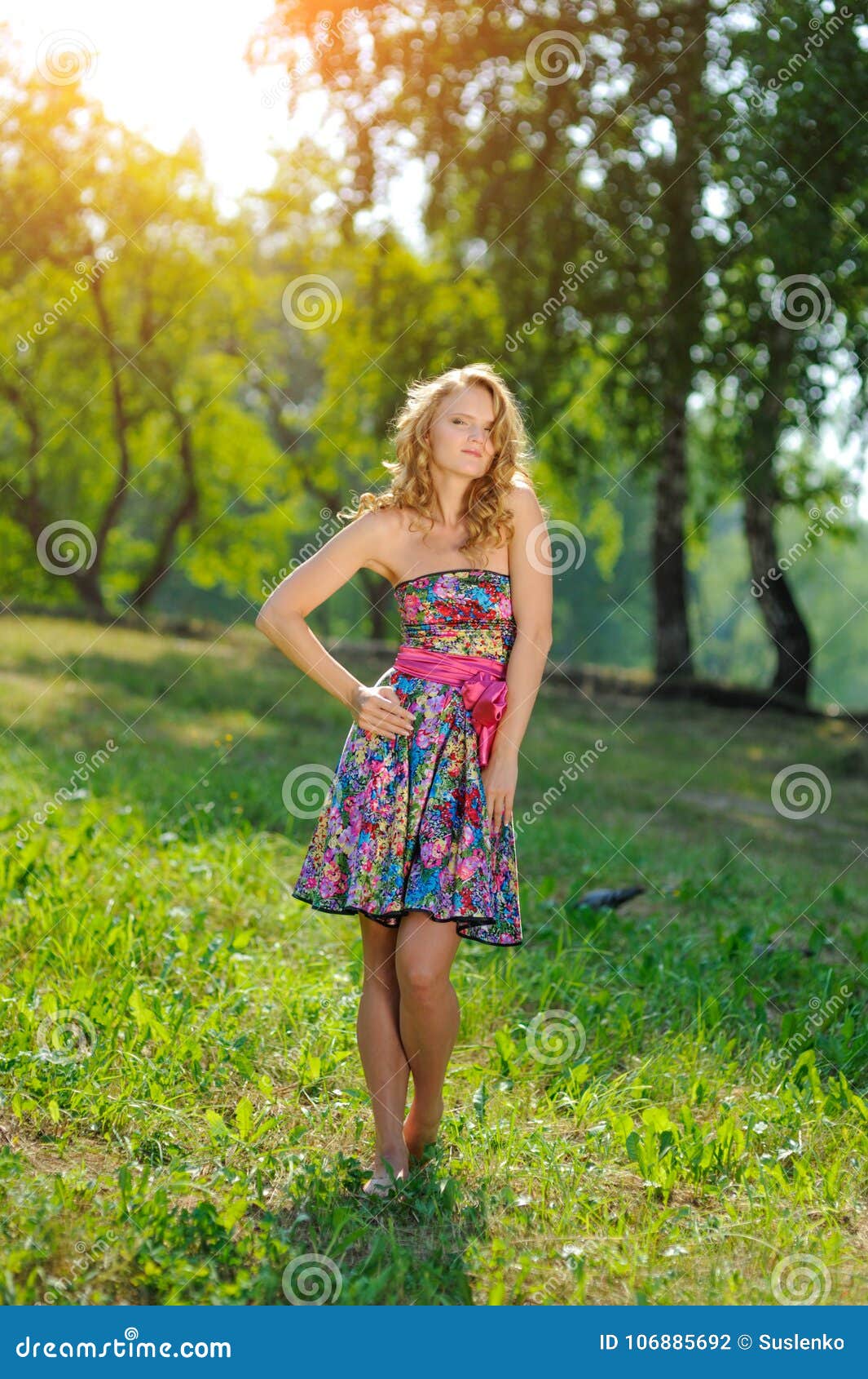 Muchacha Rubia Joven En El Vestido Colorido Brillante Que Presenta En Un Parque Del Verano En