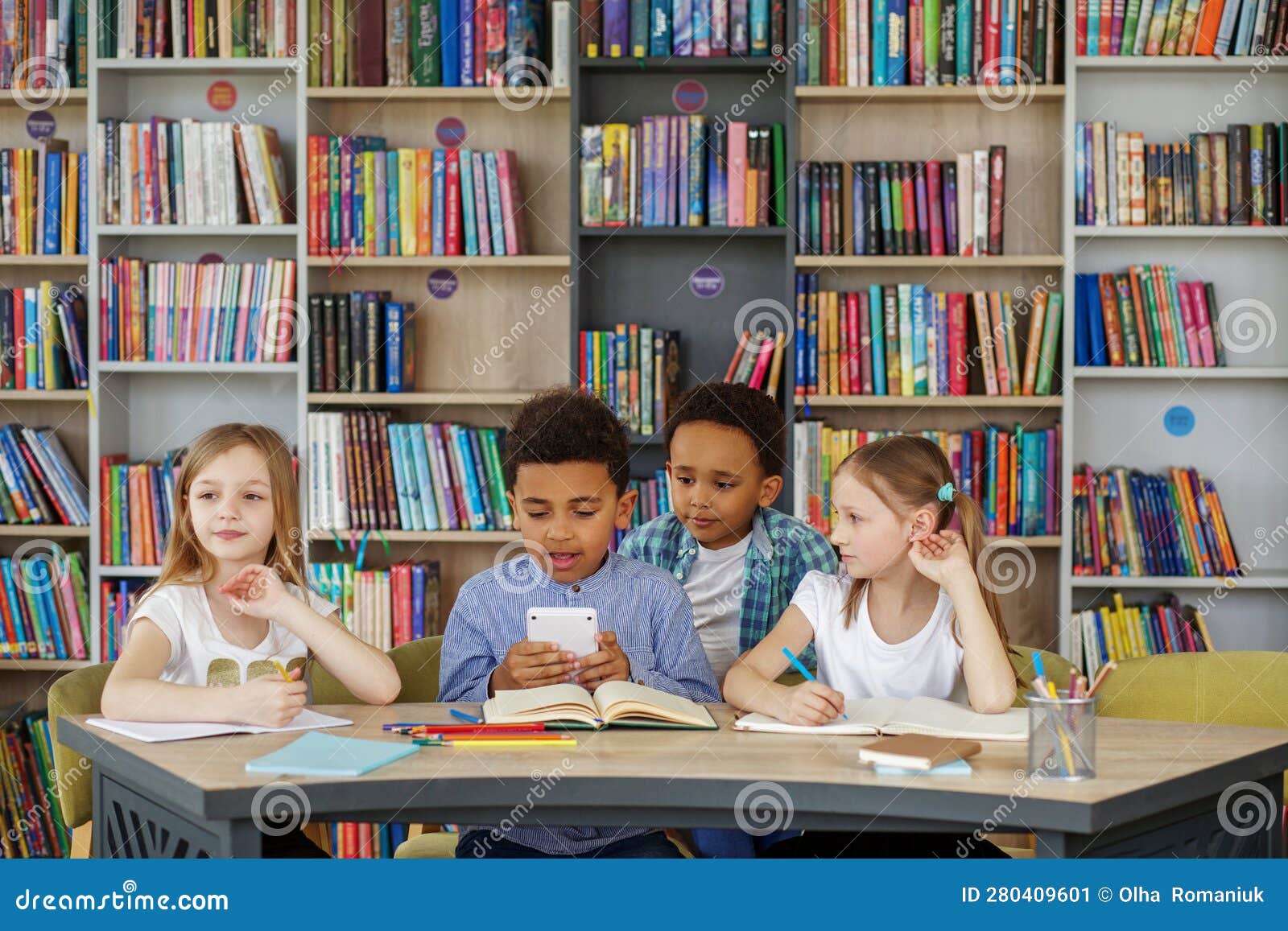 Multi-ethnic Pupils Study and Write at Table in Library or Classroom ...