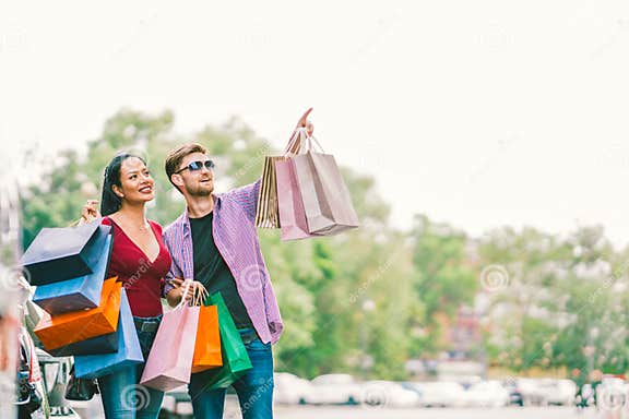 Multiethnic Couple With Shopping Bags Man Pointing At Copy Space On