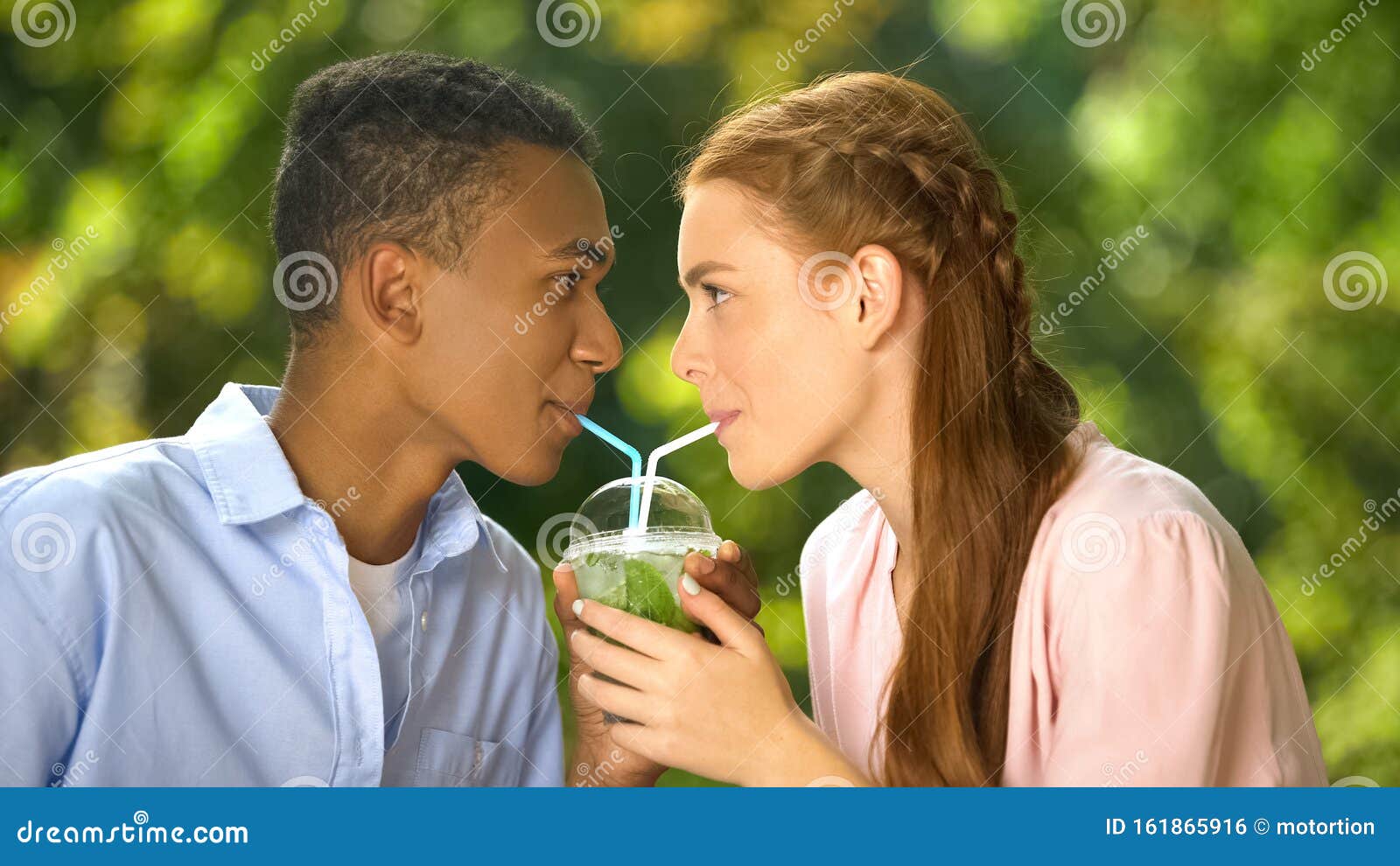 Multiracial Couple Drinking Fresh Cocktail Through Straws Looking Each