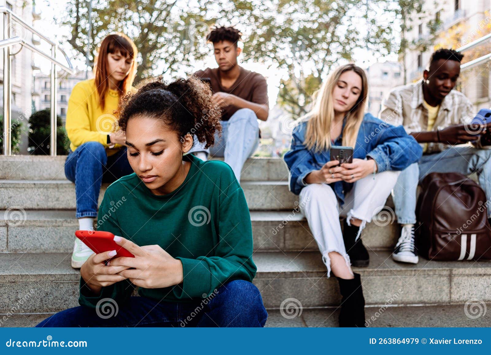 Multiracial Young Friends Using Smartphone Sitting Outdoors Stock Image